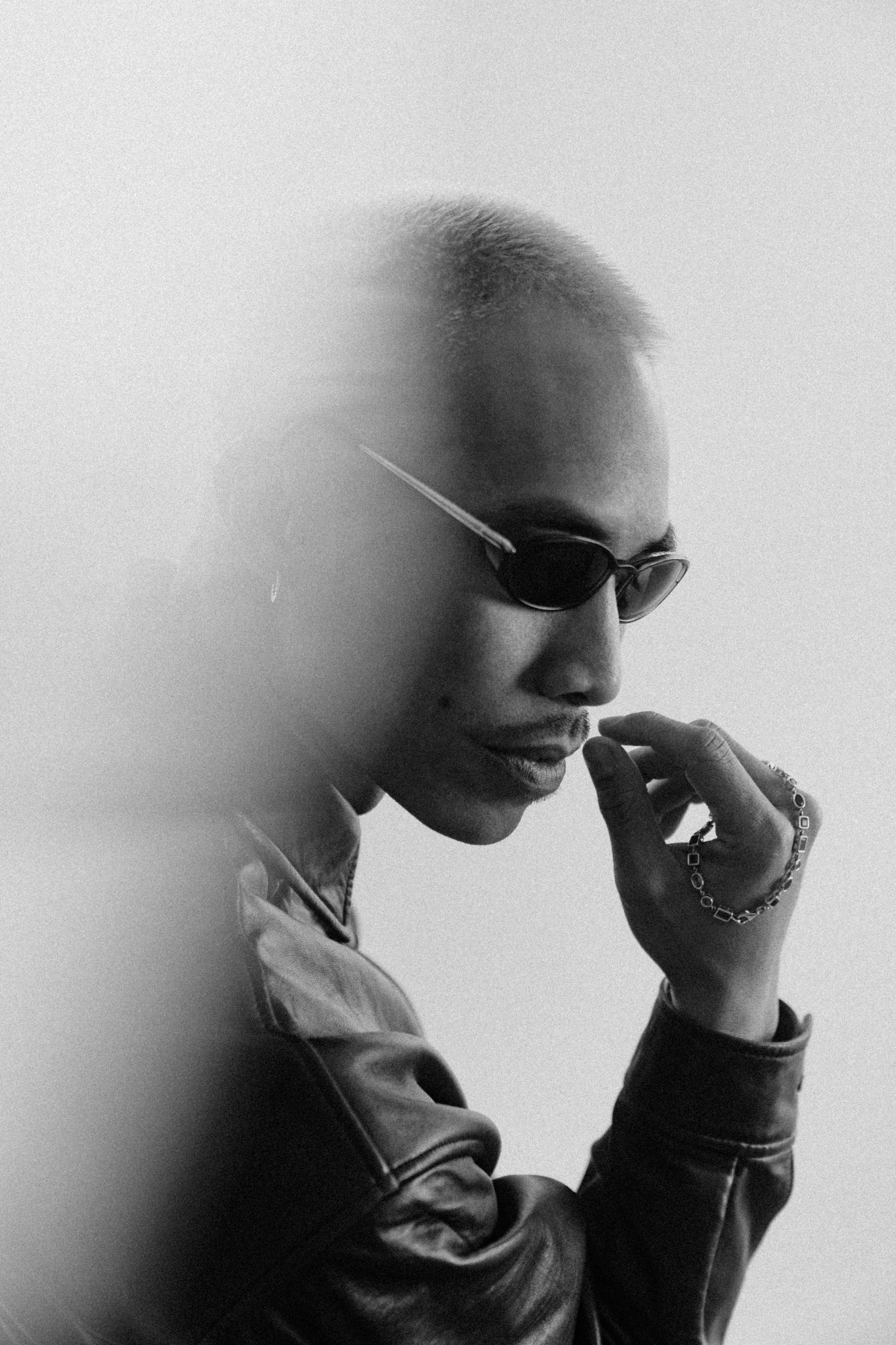 A monochrome portrait featuring a stylish individual in sunglasses, lost in thought, with a soft focus effect adding depth to the composition.