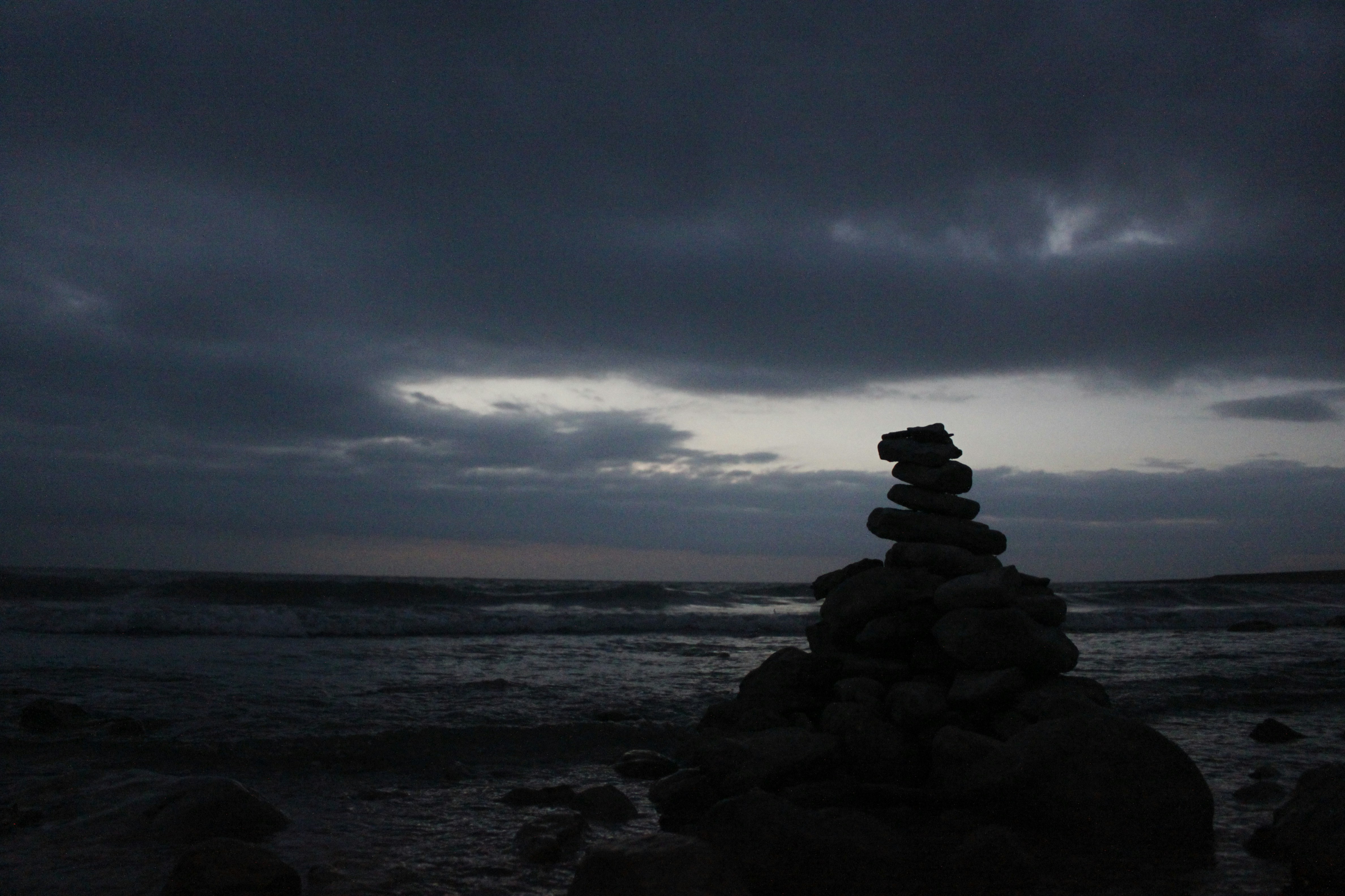 Rocas apiladas en una playa oscura y nublada al atardecer. foto ...