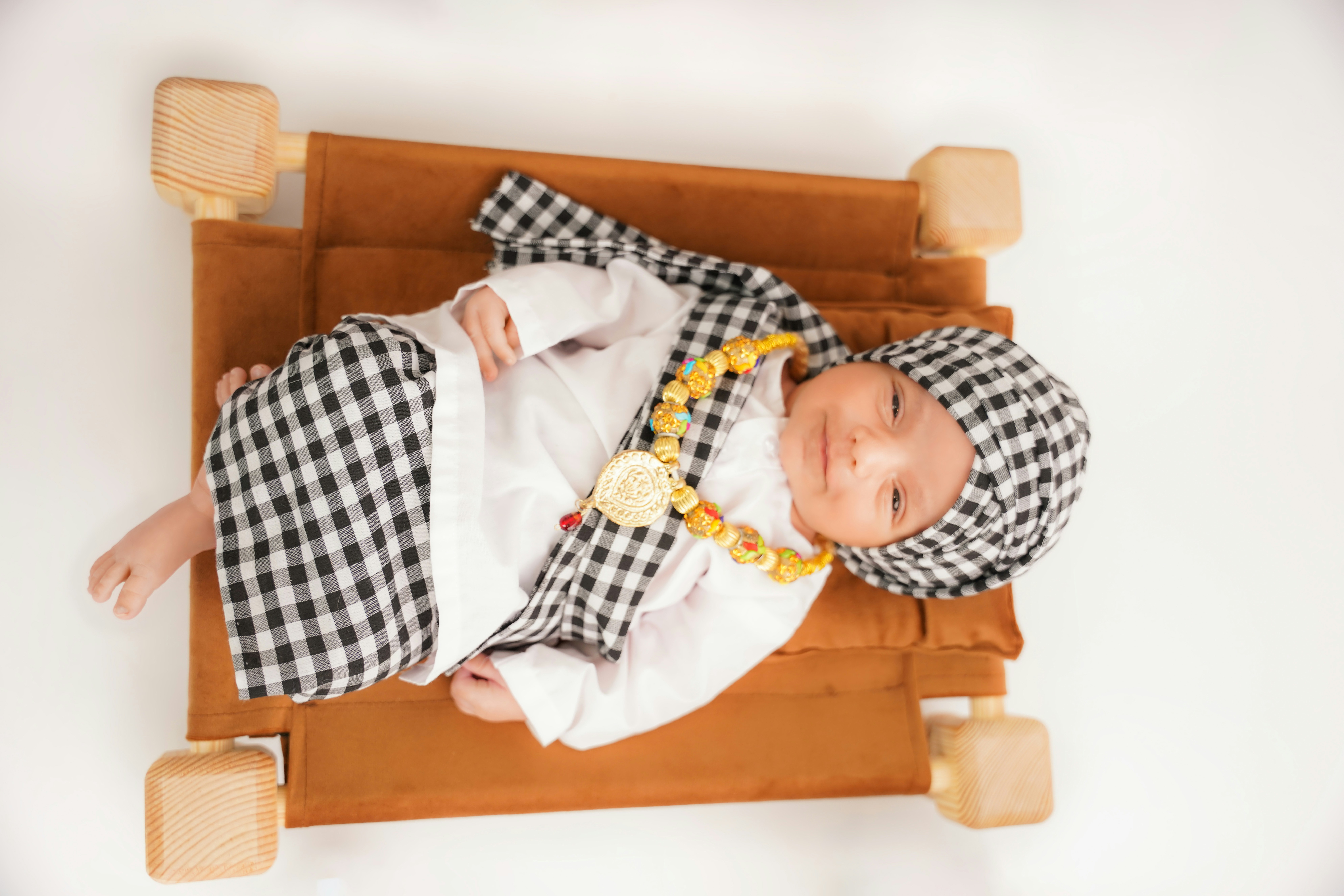 Newborn baby dressed in traditional attire on a brown mat.