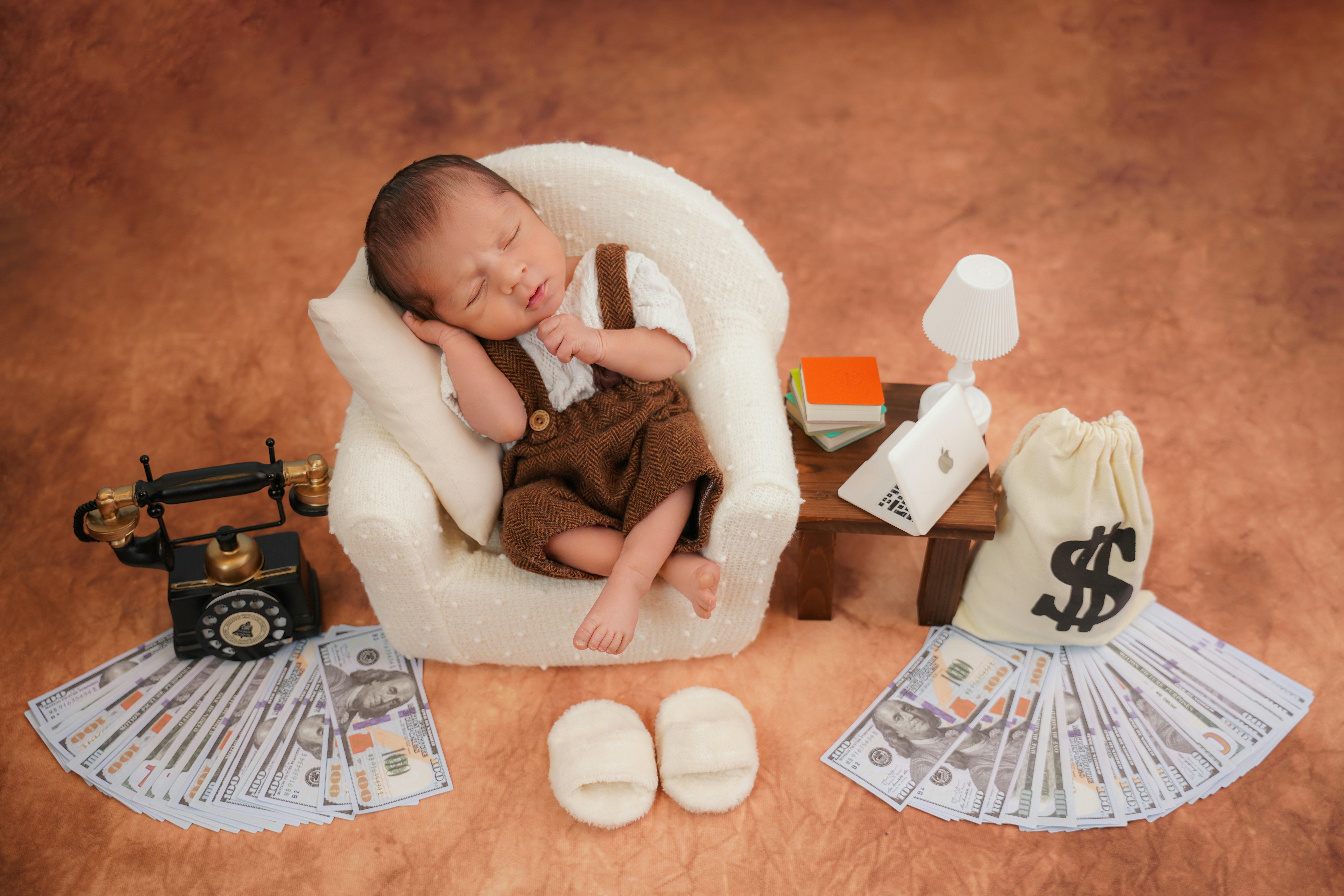 Newborn baby sleeps in tiny chair with money props.