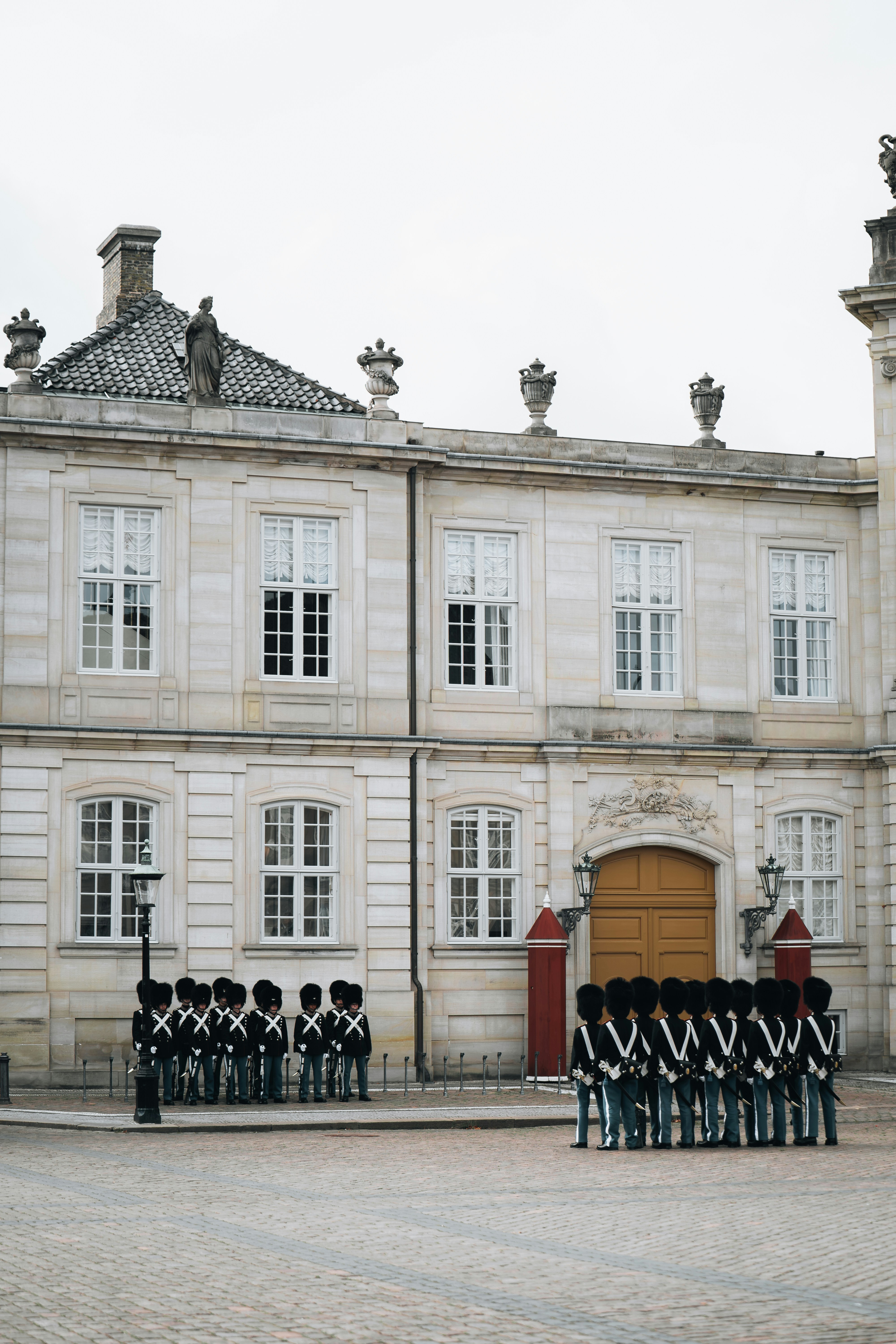 Royal guards in traditional uniforms stand in formation outside a historic building, capturing a ceremonial atmosphere.