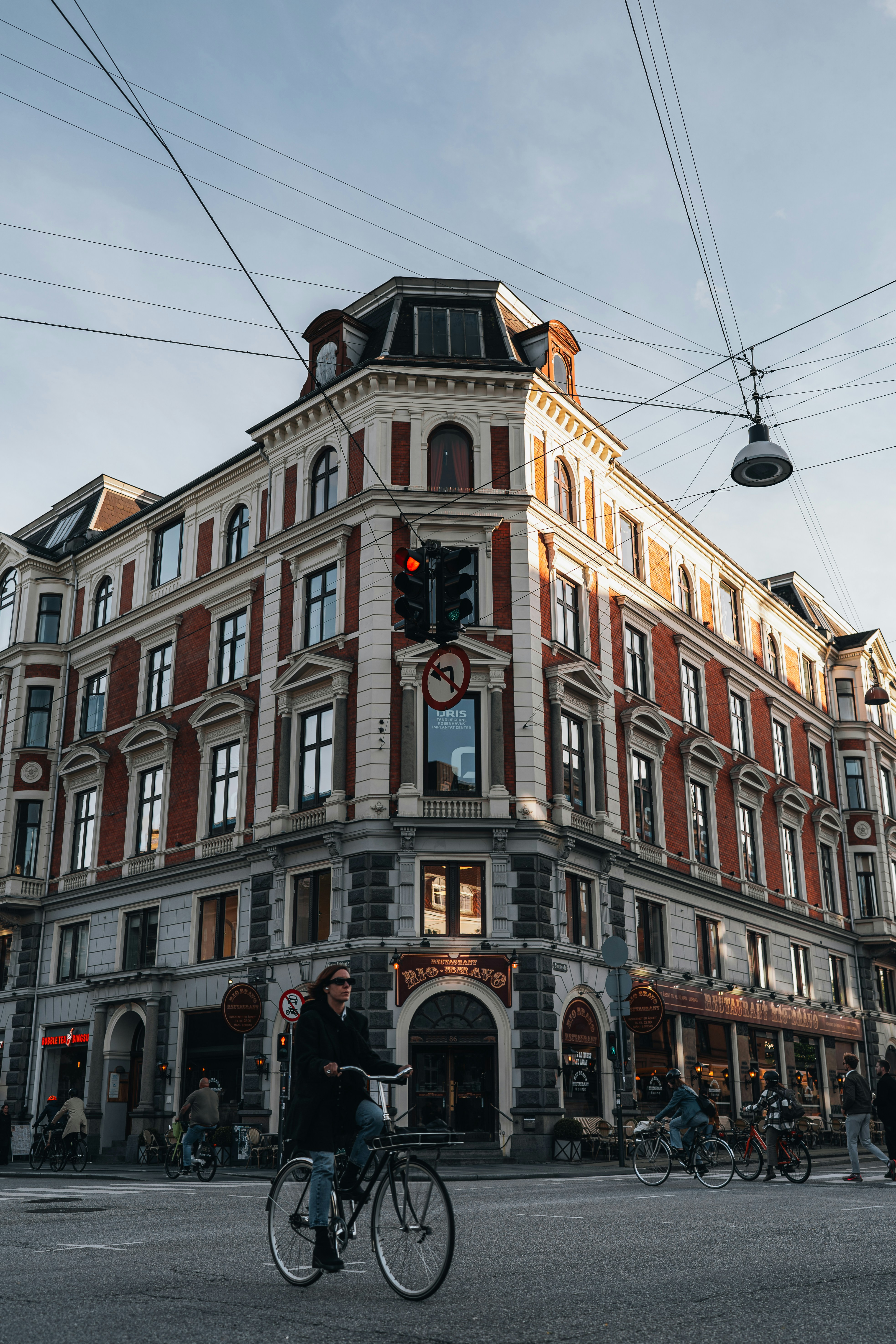 A cyclist navigates a bustling intersection with a historic building in the backdrop, showcasing urban life and architecture. The scene captures the essence of city commuting.