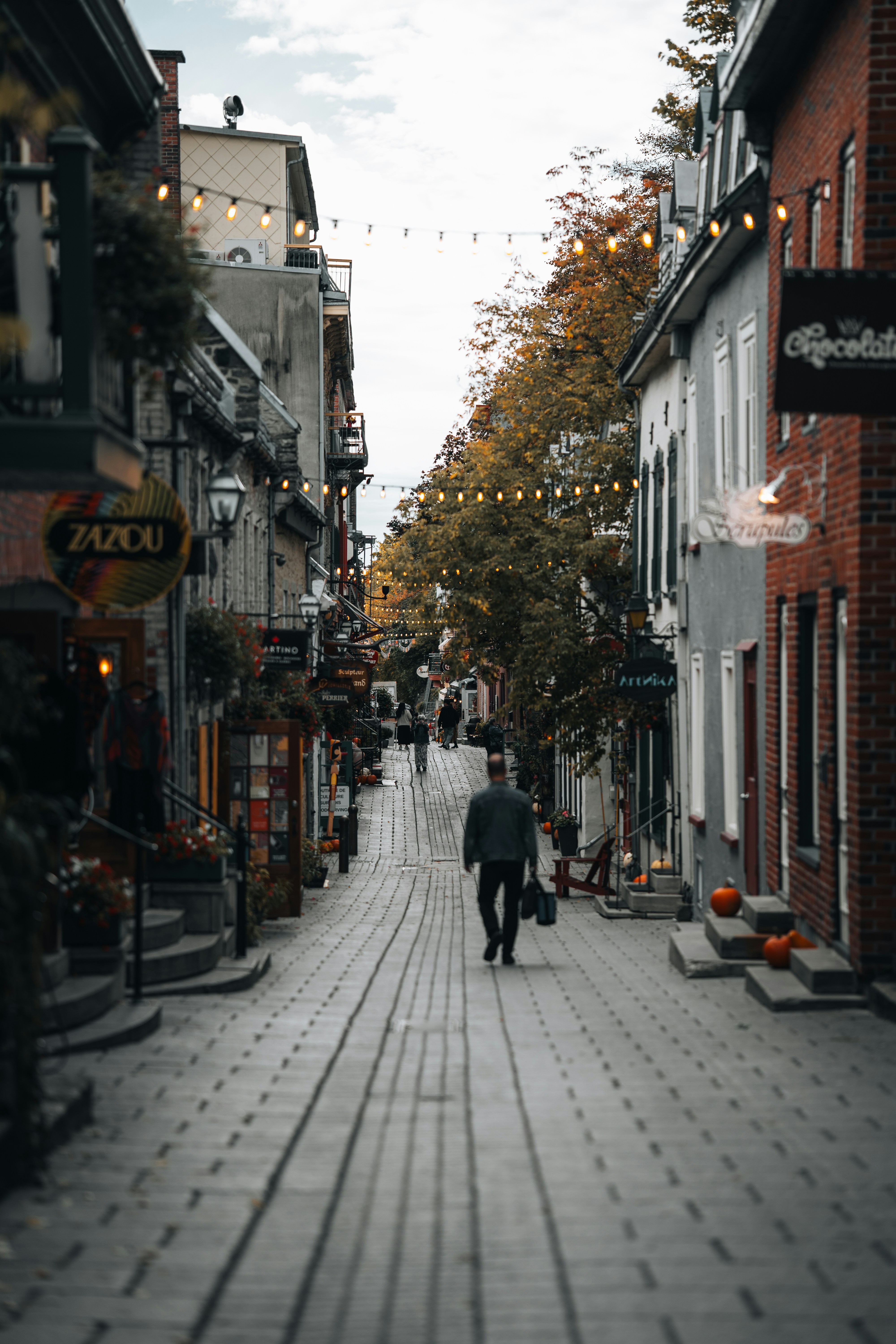 Man walks down a cobblestone street lined with shops.