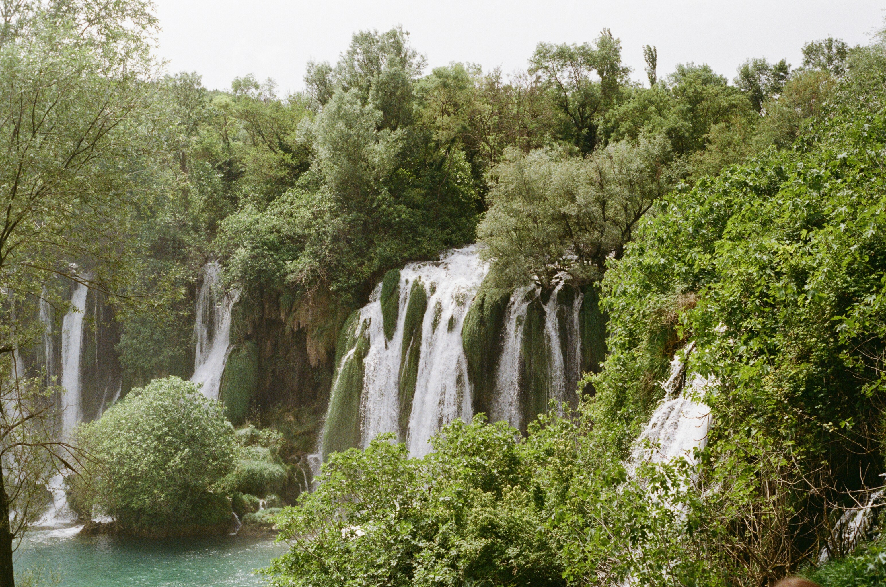 Lush green forest surrounds cascading waterfalls.