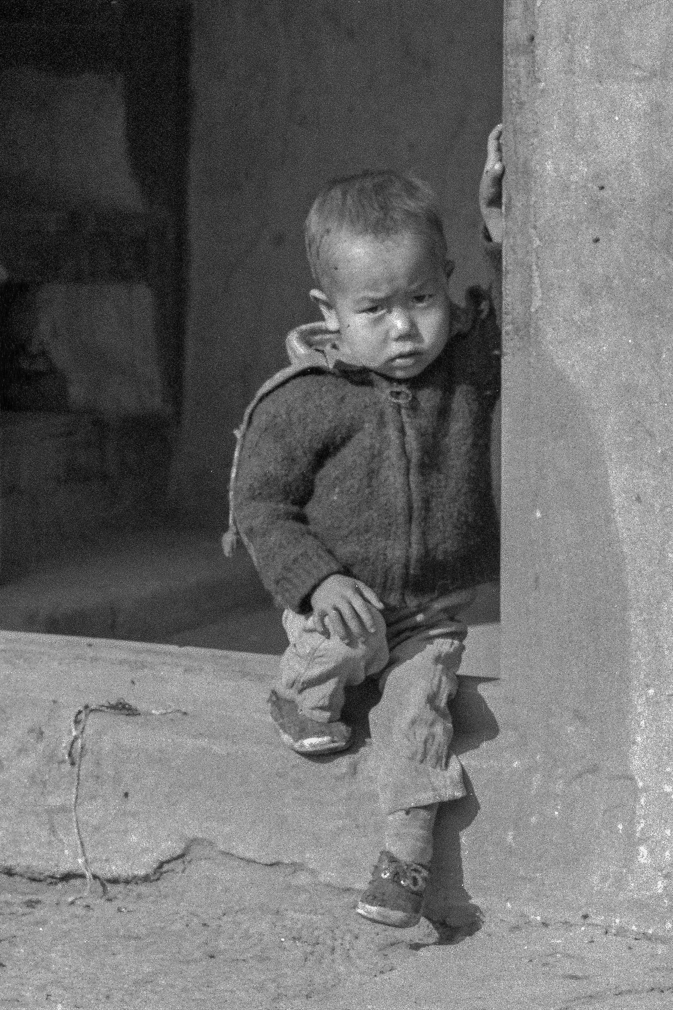 Young child sitting on a doorway step, gazing thoughtfully into the distance. The scene captures a blend of curiosity and contemplation.