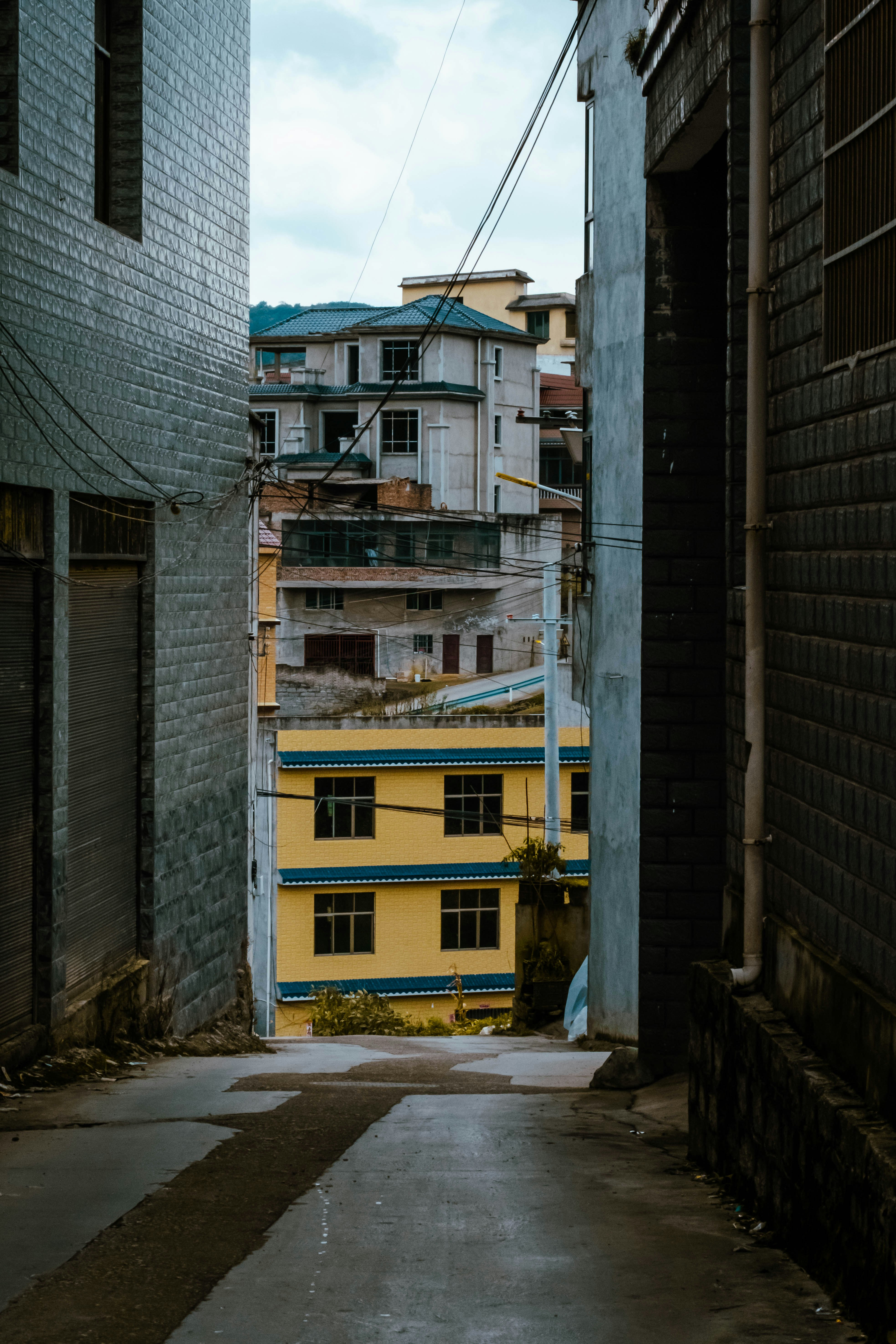 Narrow alleyway between buildings leading to distant houses.
