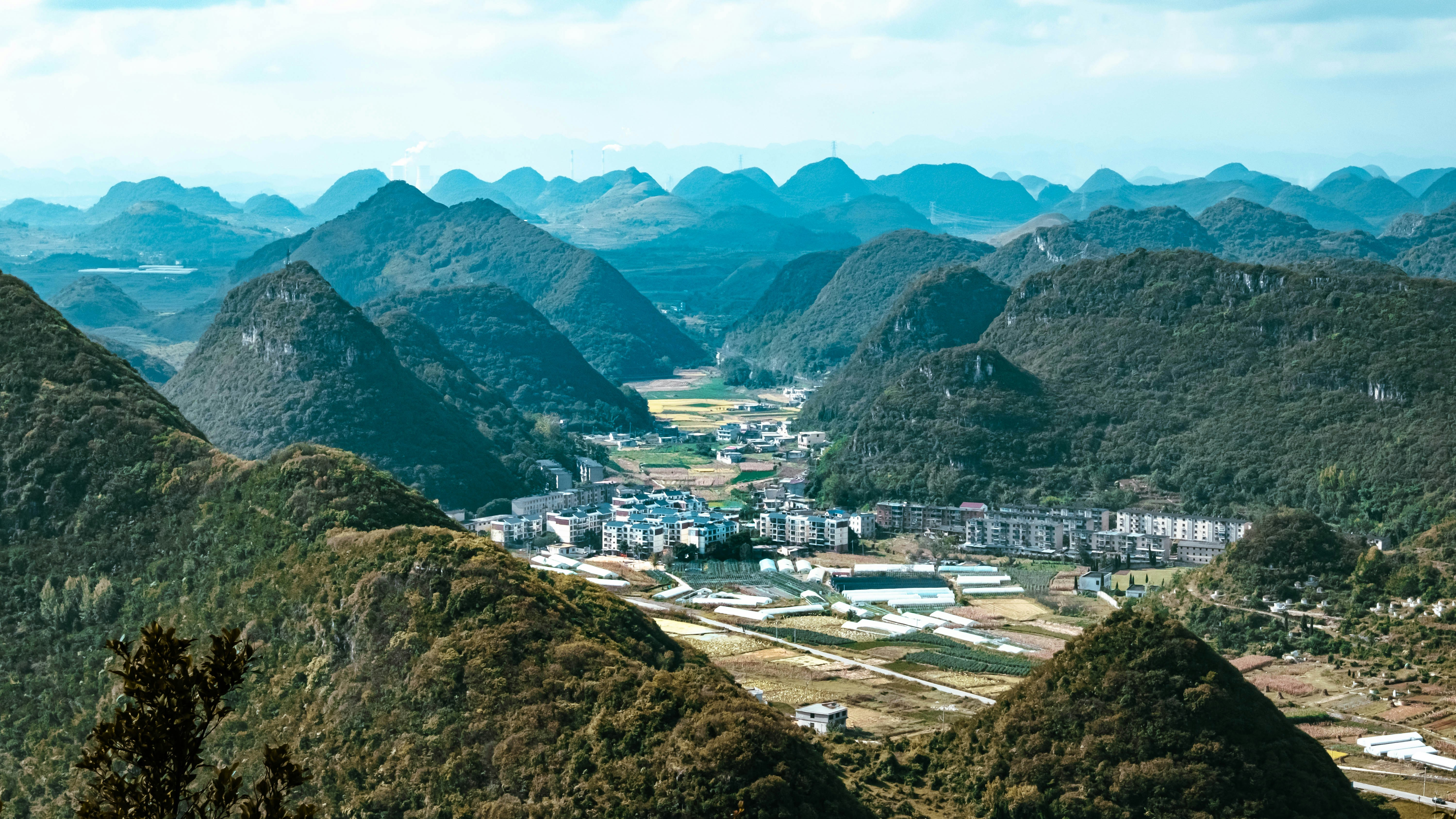 A panoramic view of lush valleys surrounded by a range of rolling mountains, showcasing the interplay of nature and human habitation.