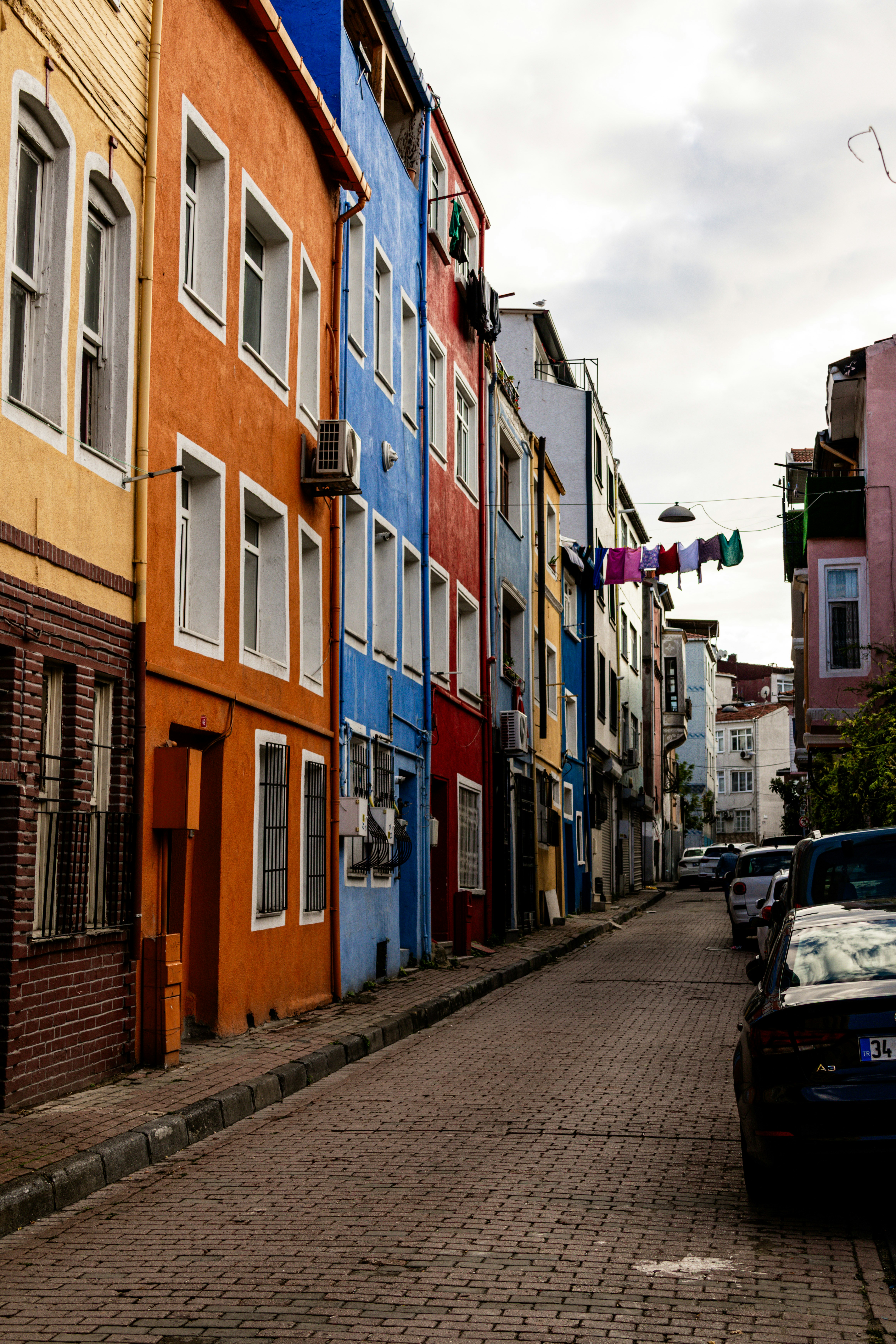 Colorful buildings line a cobblestone street with parked cars.