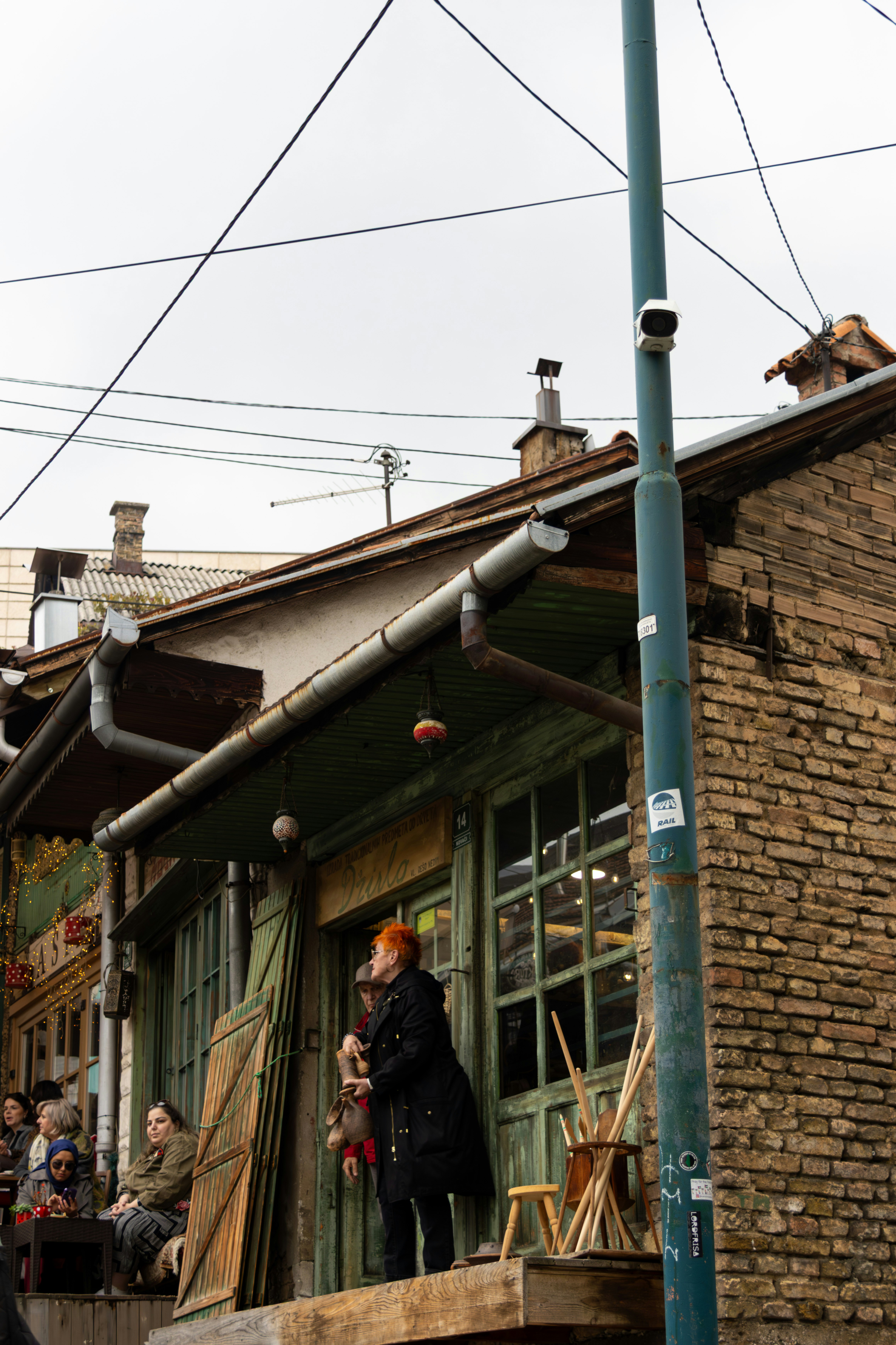 Amber-haired Figure on a Weathered Storefront Porch Beneath a Tangle of Wires