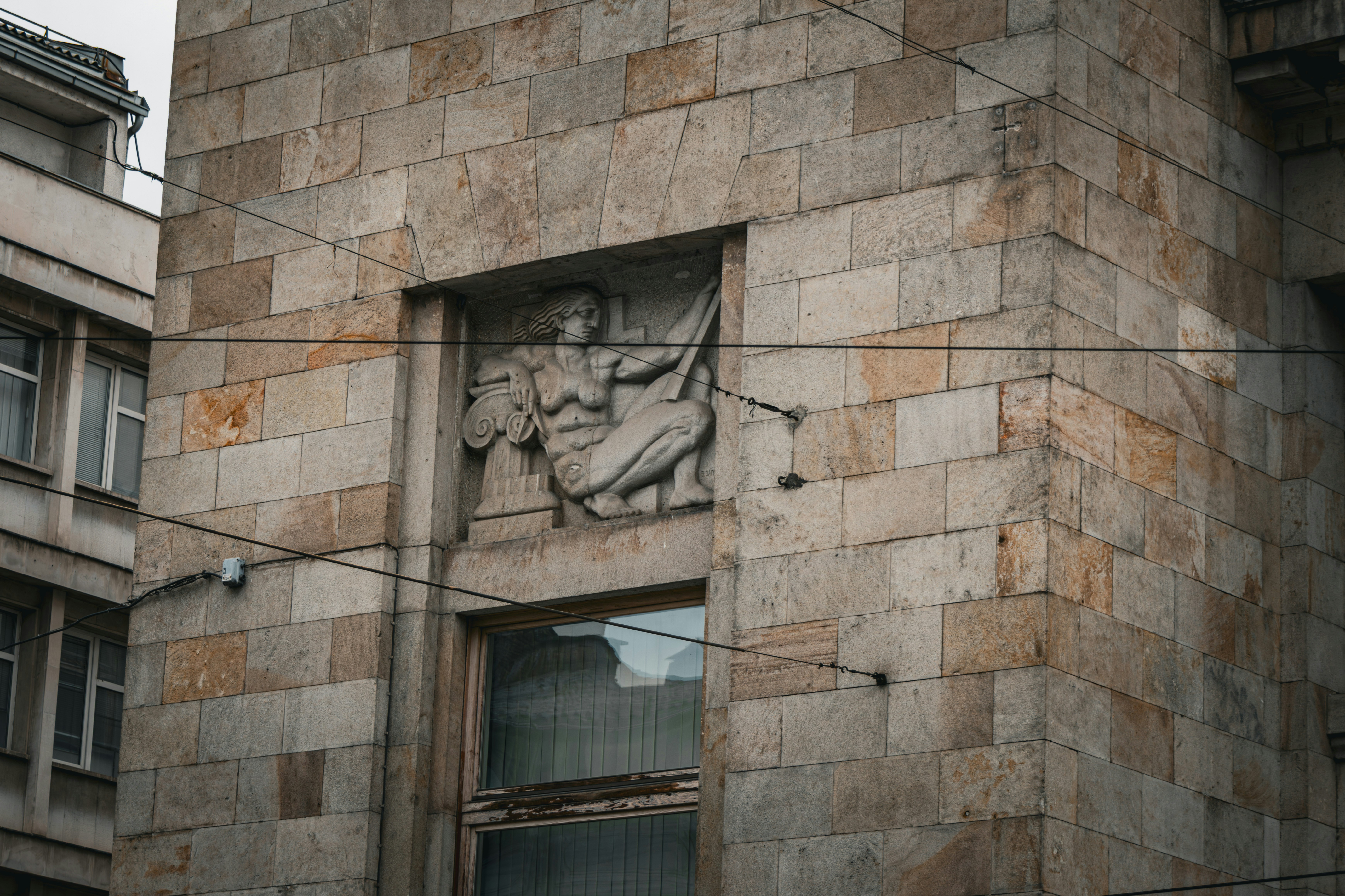 Winged Muse in Stone: Bas-Relief Framed by a Narrow Window on a Weathered Façade