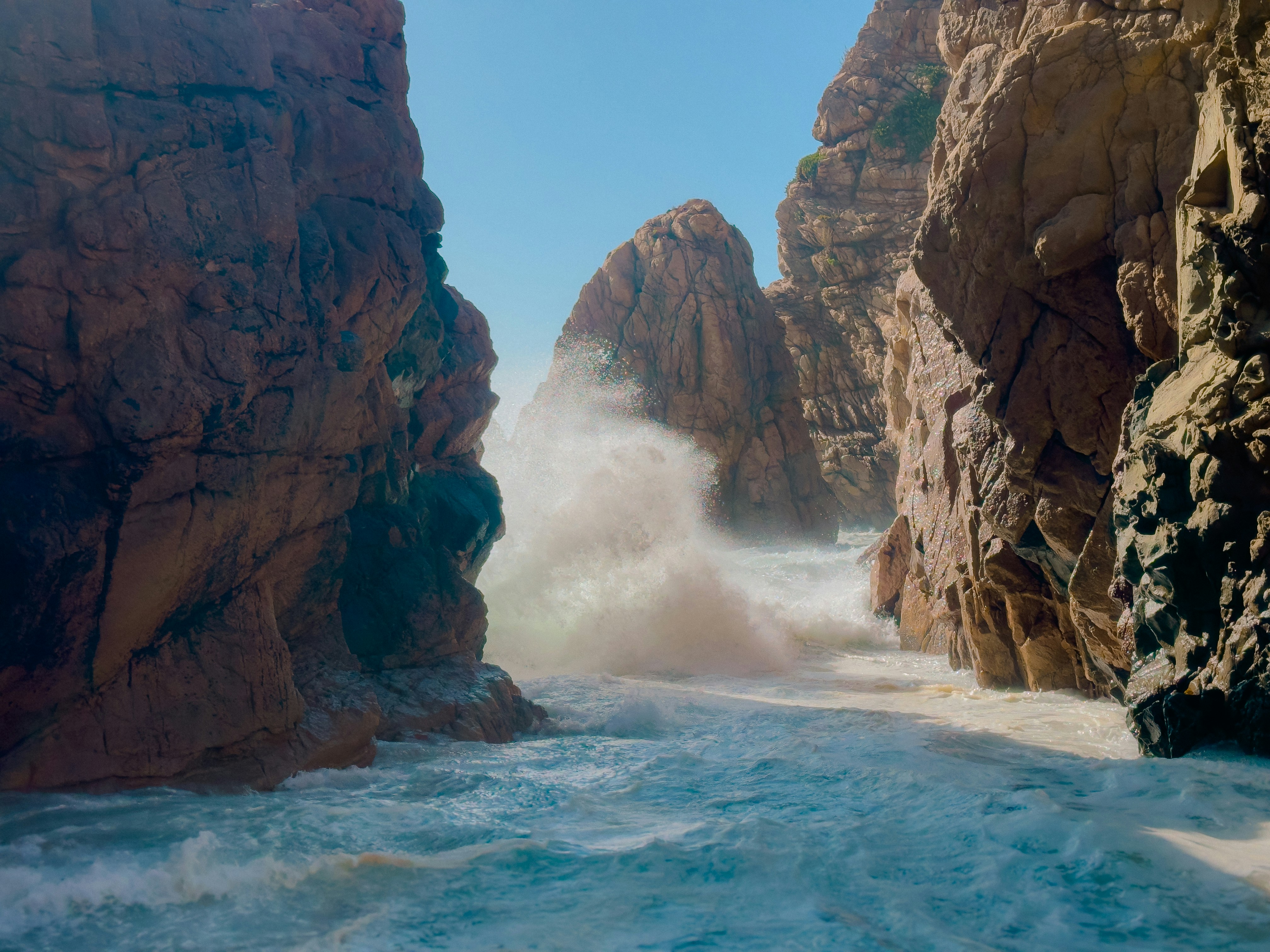 Waves crashing against rocky cliffs under a clear sky