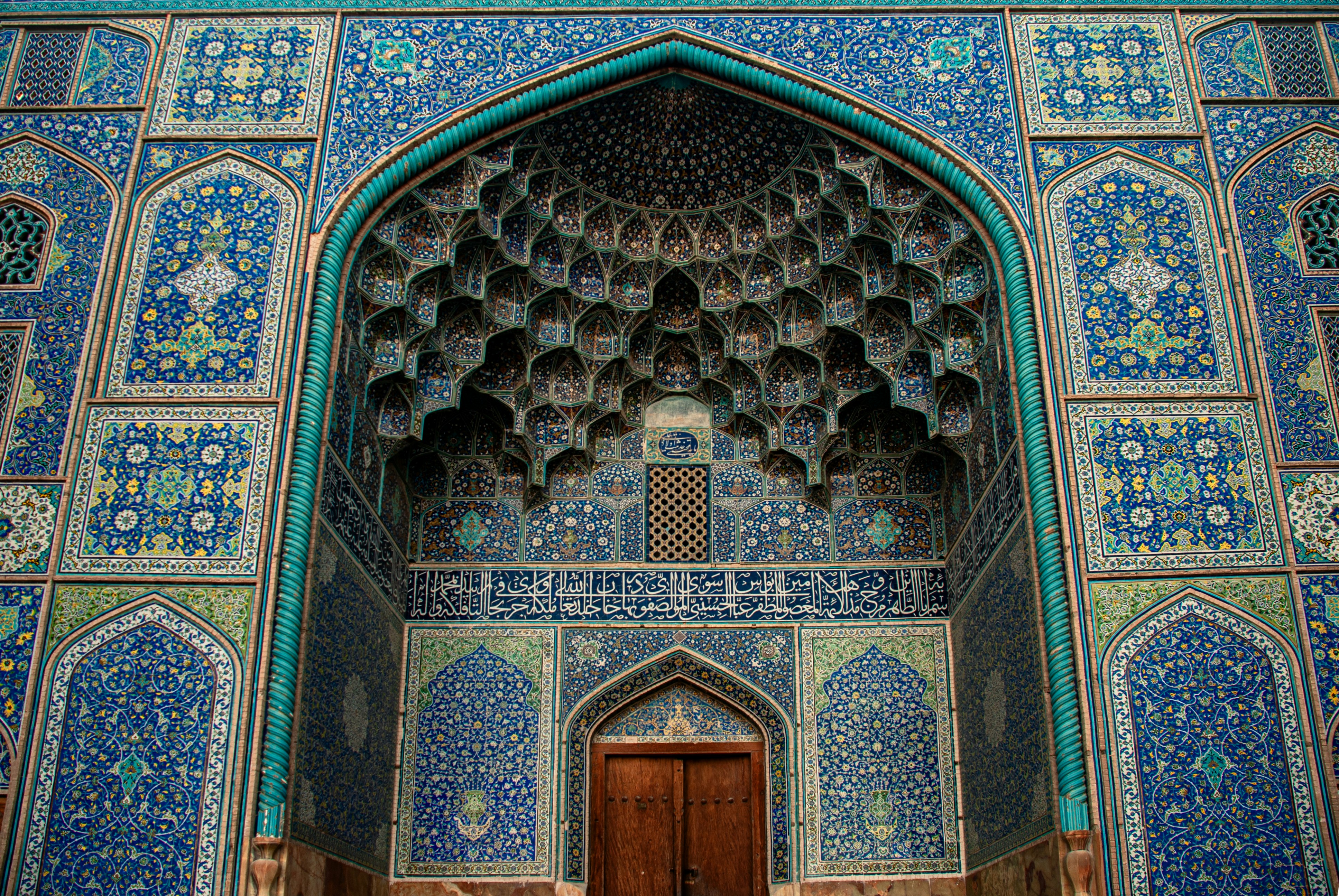 Every detail is a balance of geometry, symmetry, and rhythm — patterns repeating endlessly, yet never the same. | Intricate blue and green tilework on an arched building entrance.
