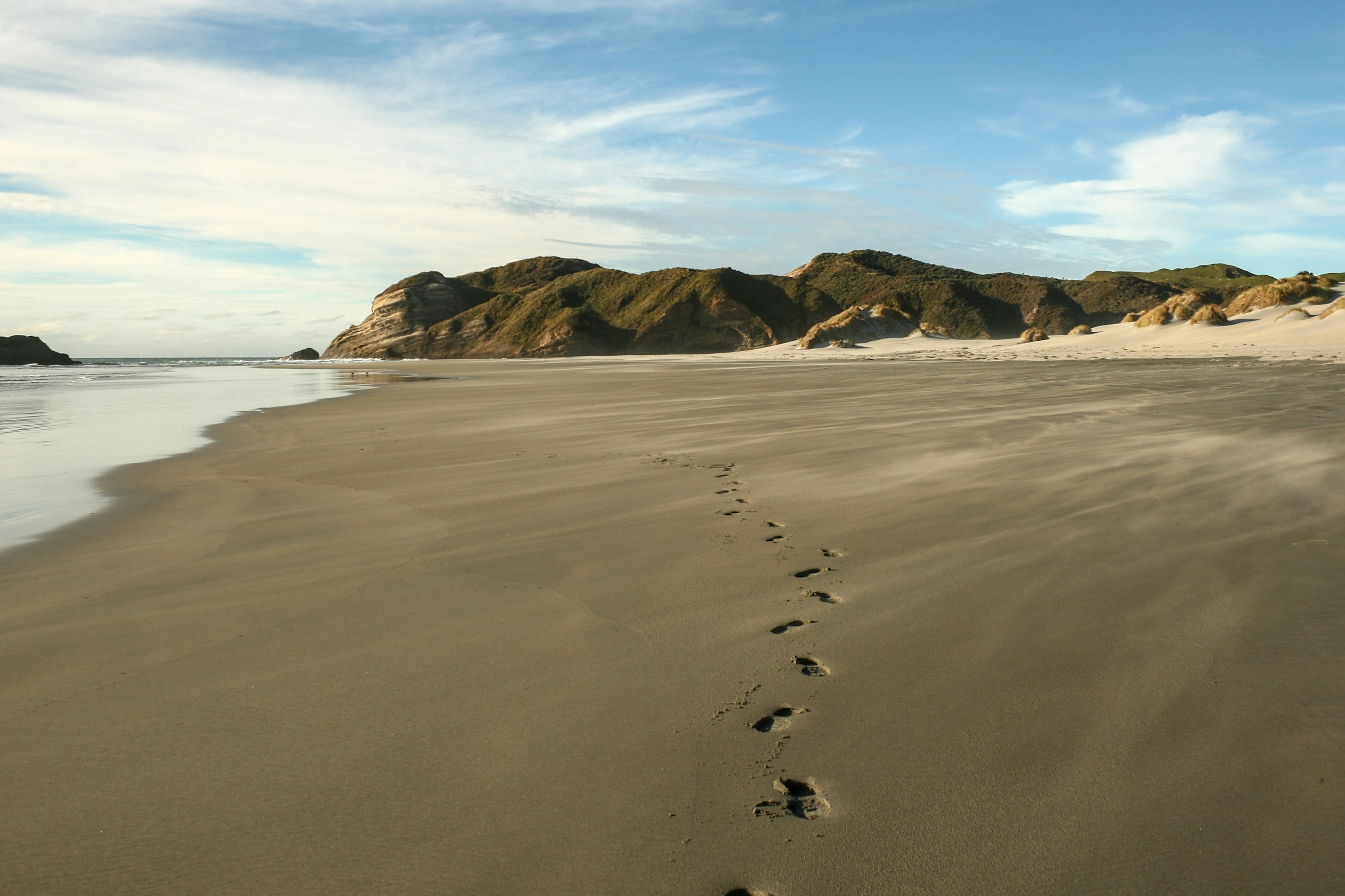 Footprints toward Wind-Sculpted Dunes Under a Quiet Coastal Sky