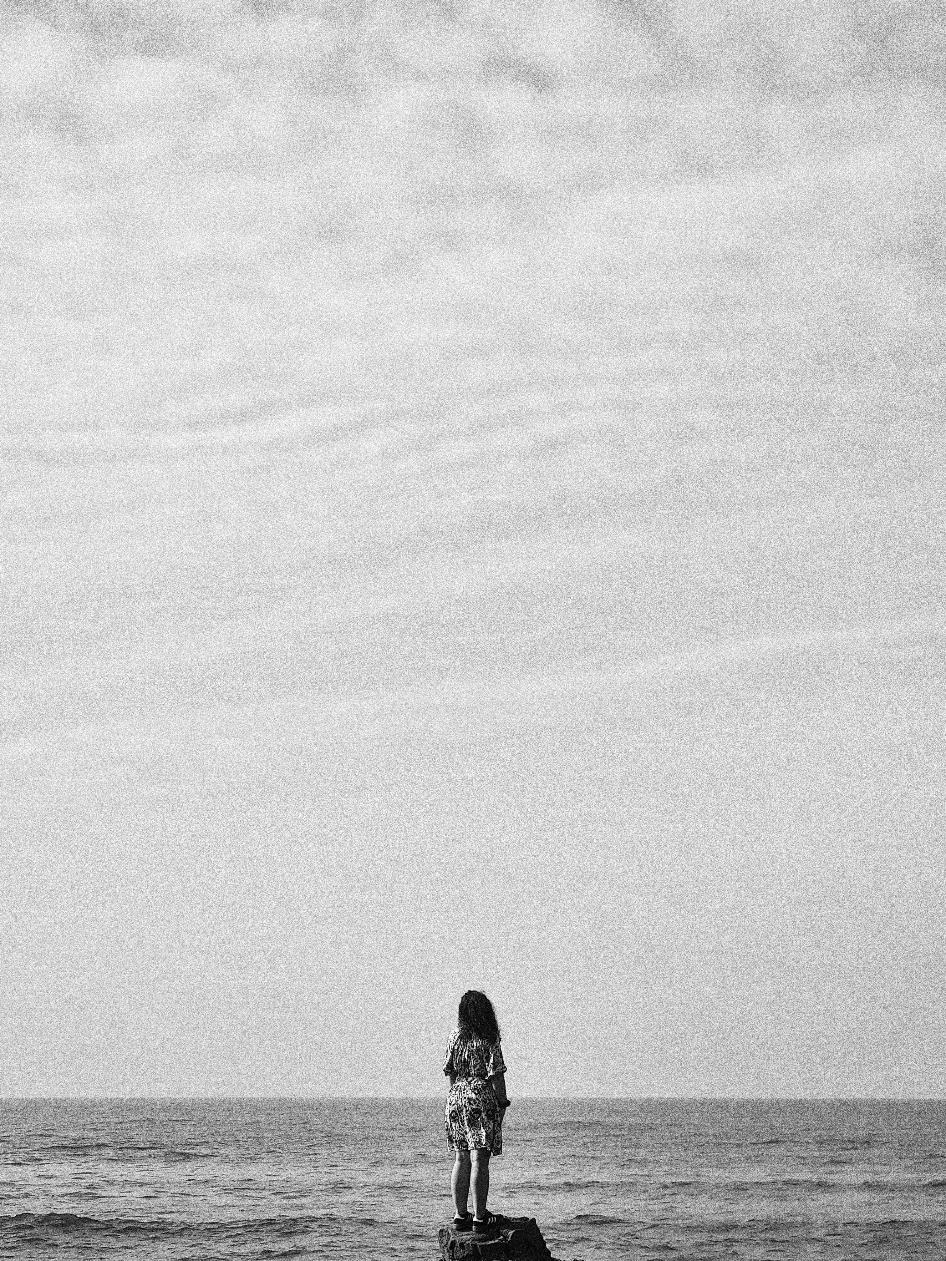 a woman standing in front of beach | A lone child stands on a rock by the sea.