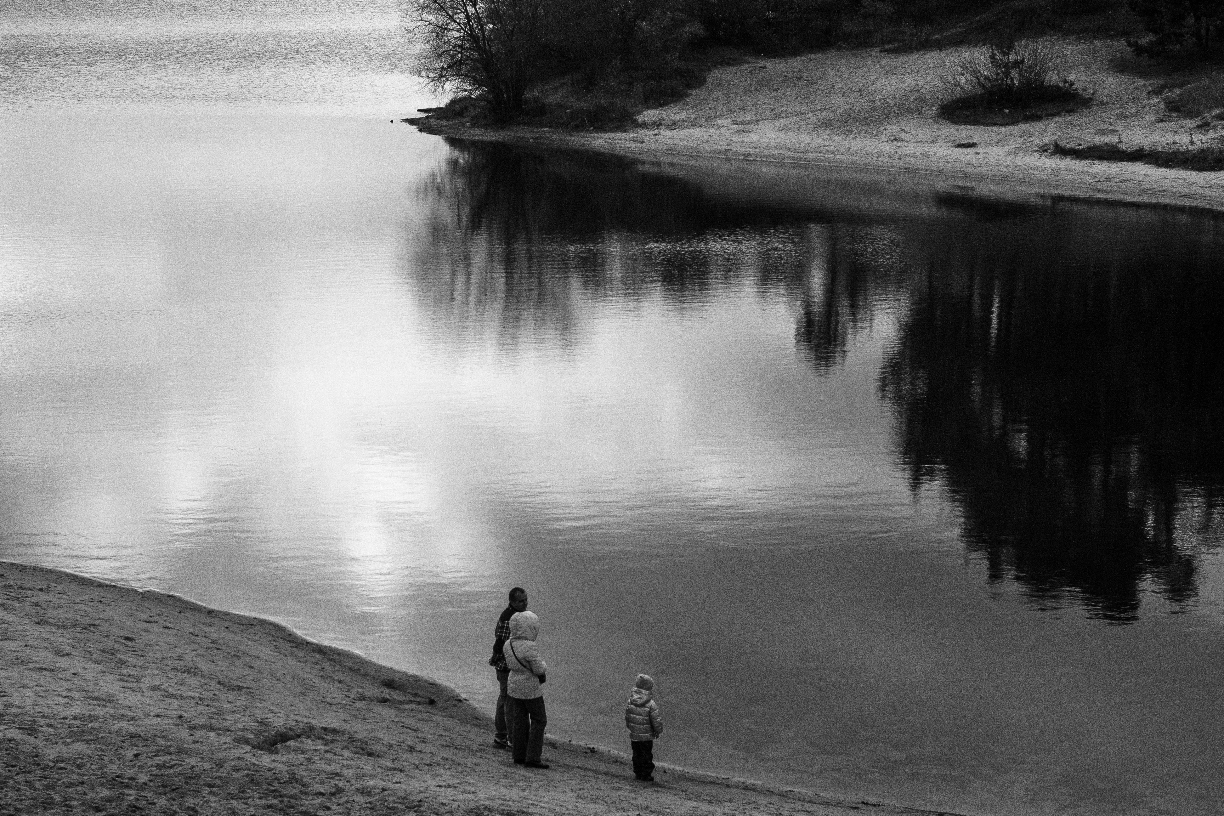 Two people and a child stand by a calm lake.