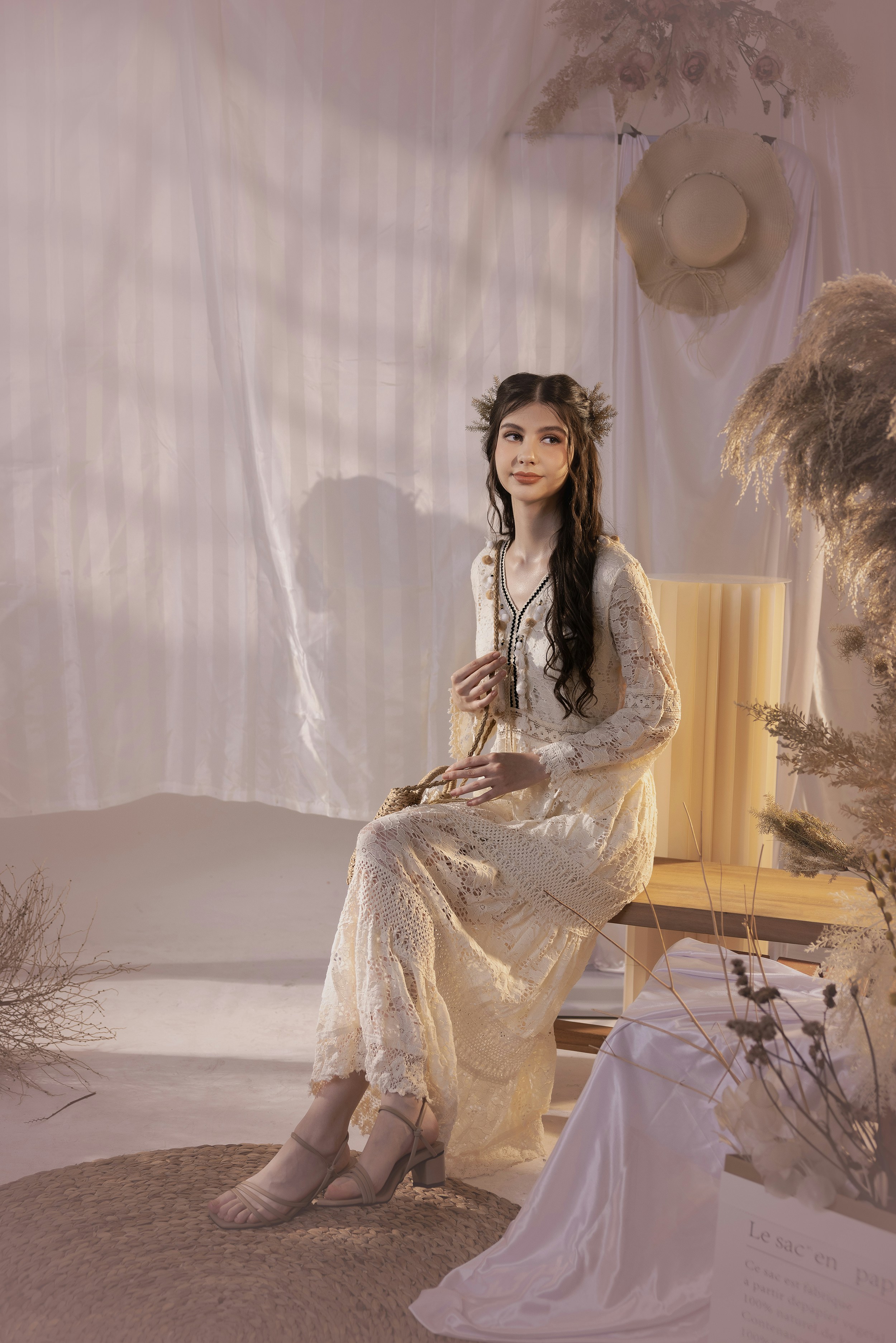 Young woman in a white lace dress sits indoors.
