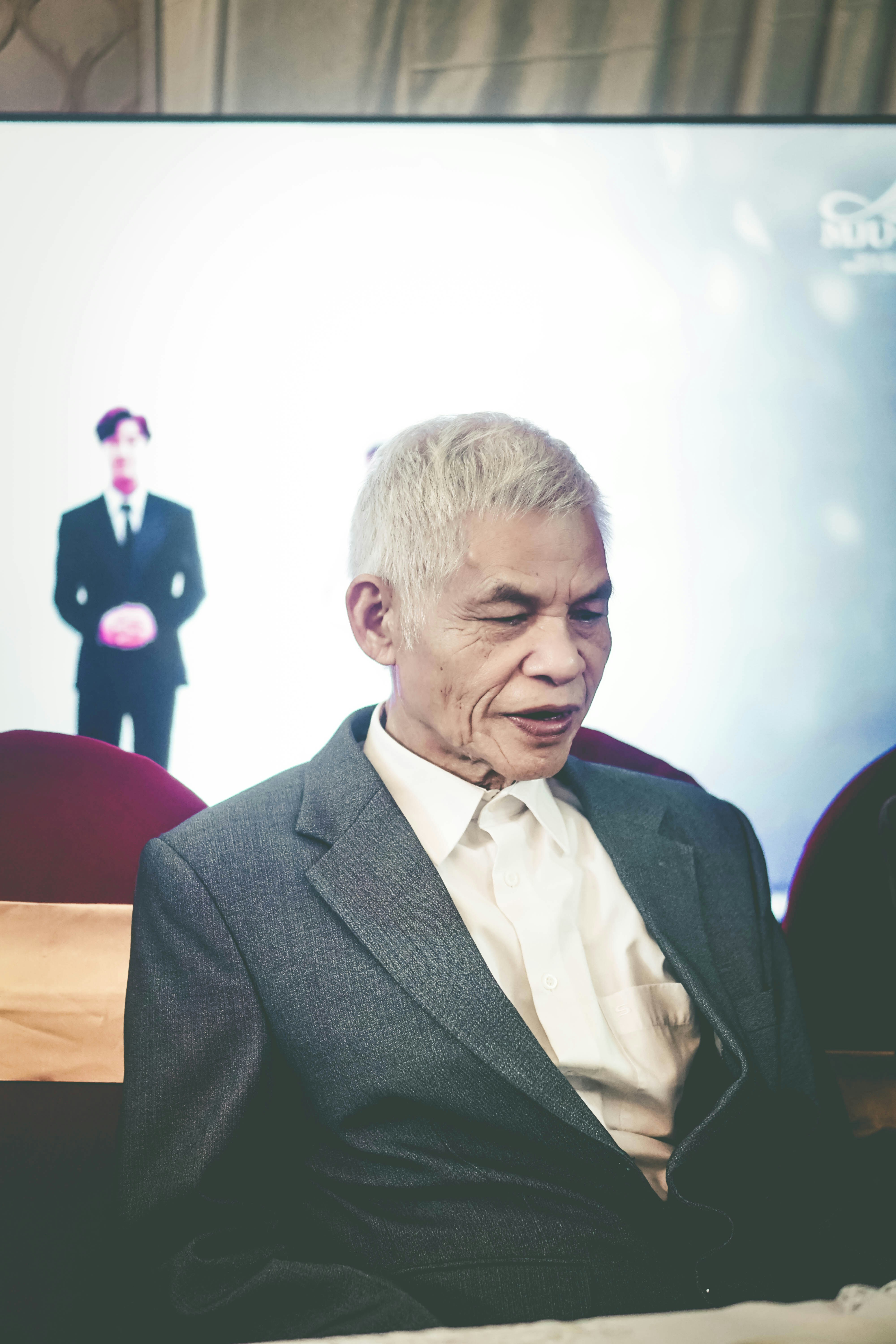 Onstage Contemplation: An Elder in a Gray Suit Before a Luminous Backdrop