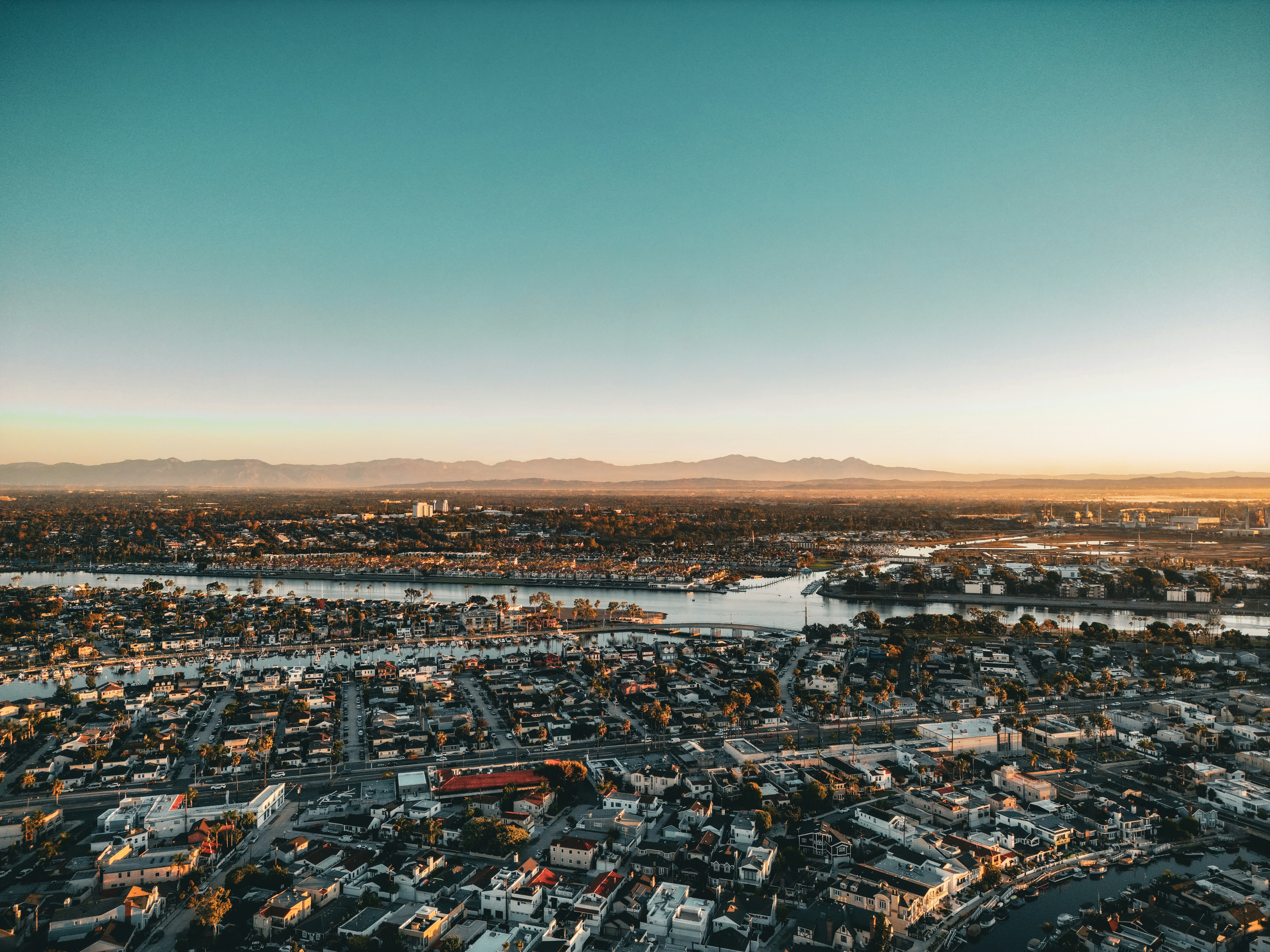 Aerial view of a sprawling urban landscape with winding waterways and distant mountains under a twilight sky.