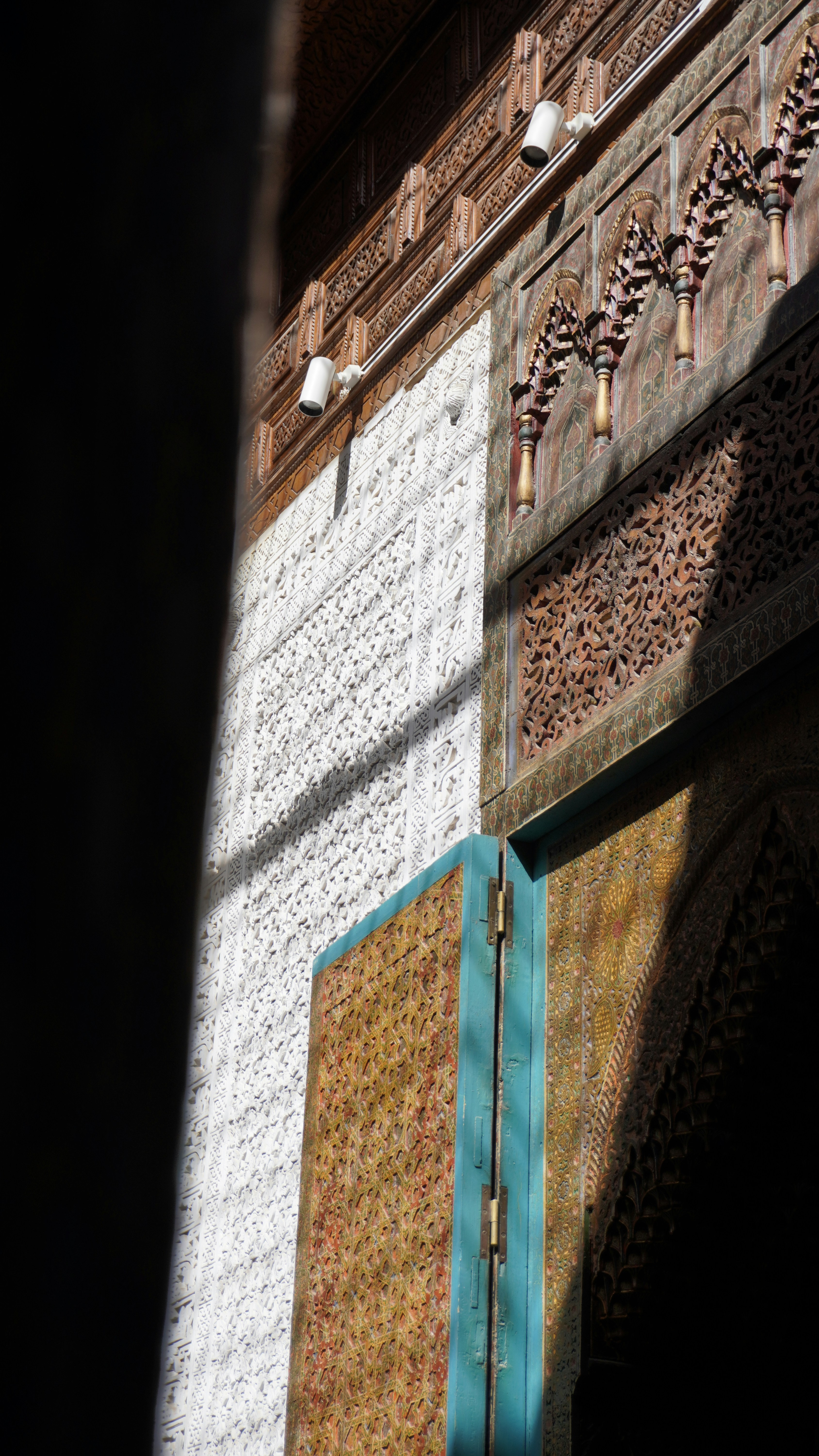 Intricately carved wooden door framed by textured stone wall, illuminated by soft sunlight, showcasing a blend of cultural artistry.