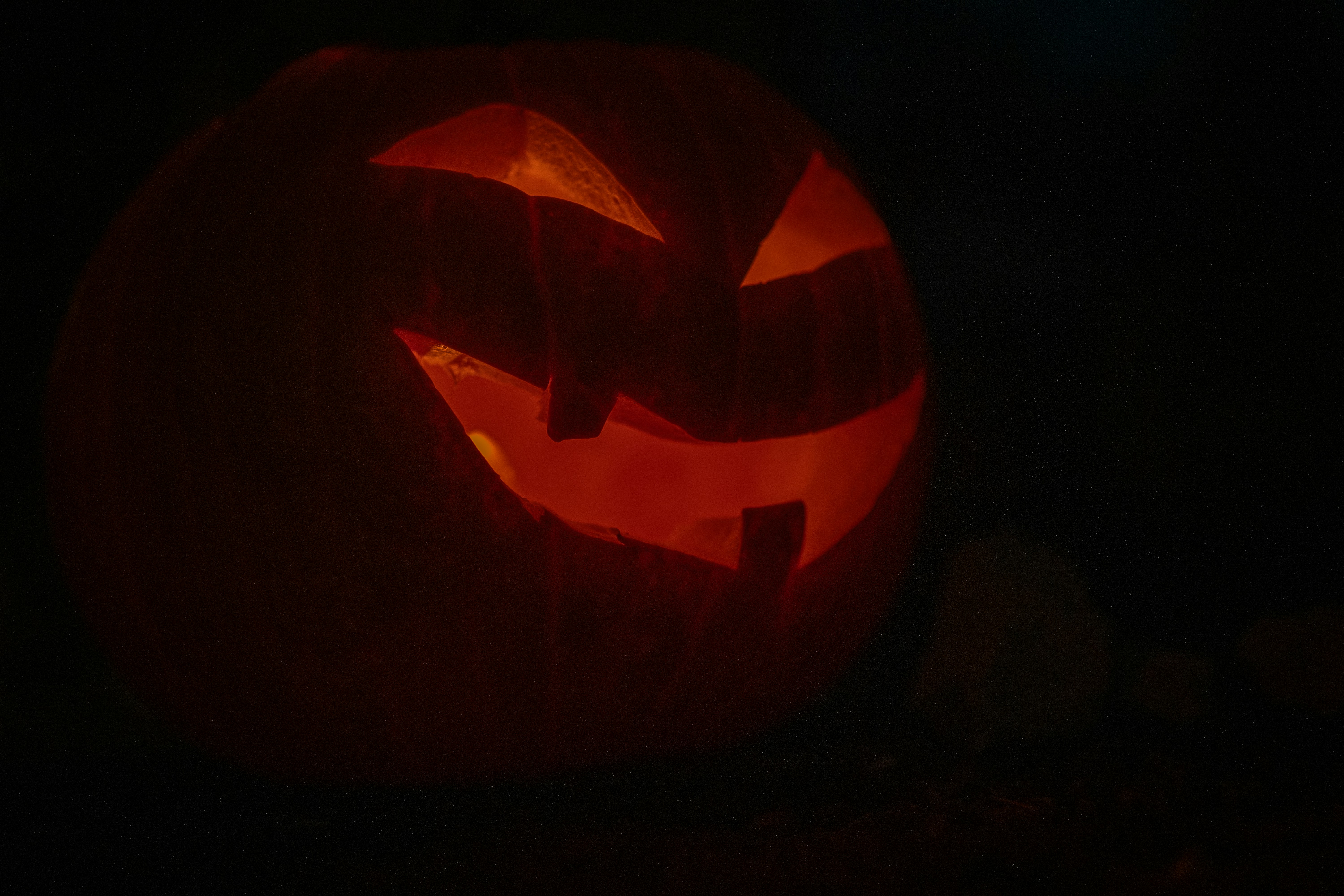 Illuminated jack-o'-lantern with a mischievous grin, casting a warm orange glow in a darkened setting.