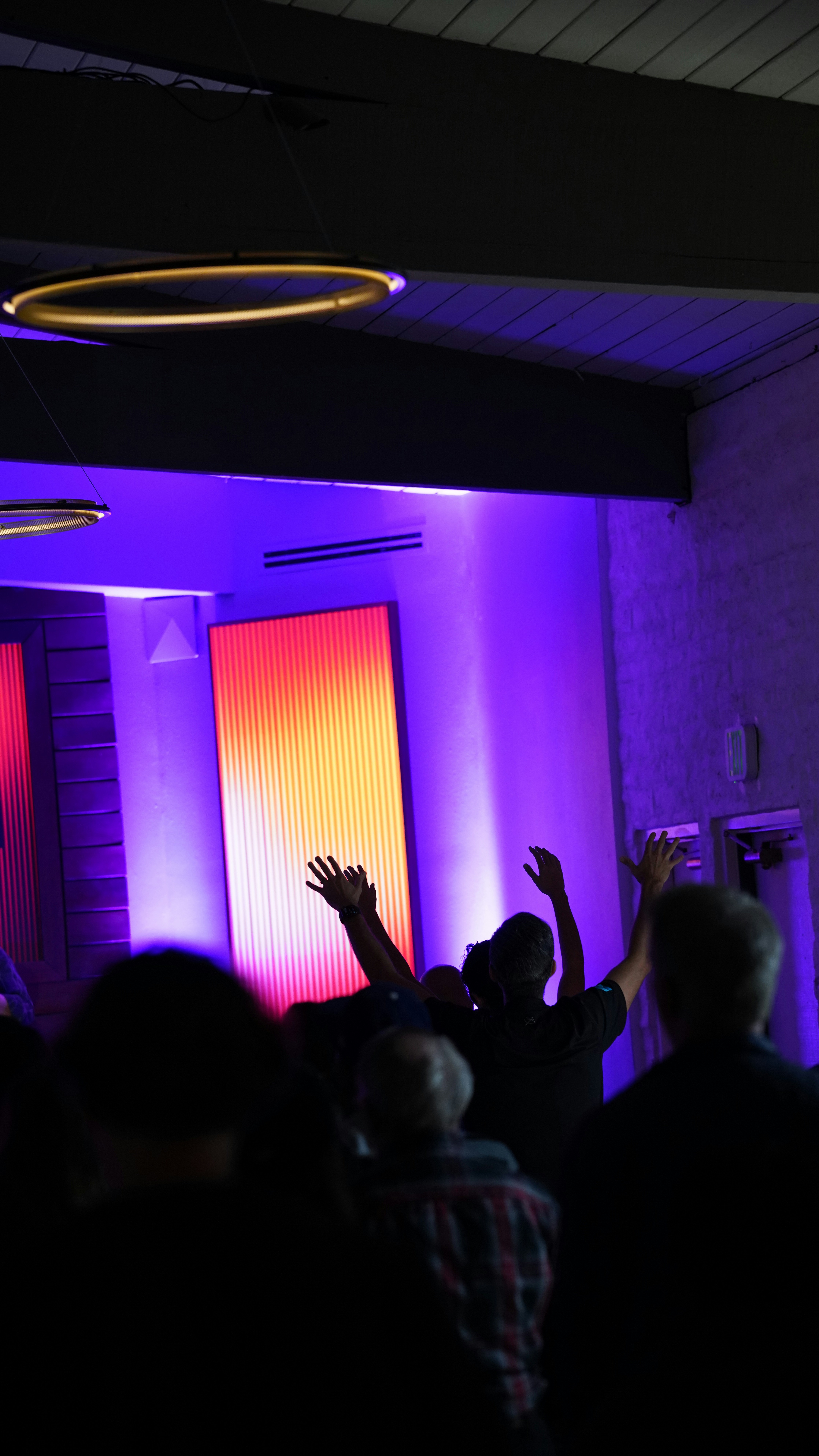 Audience members raise their hands in a moment of connection under colorful lighting in a lively venue.