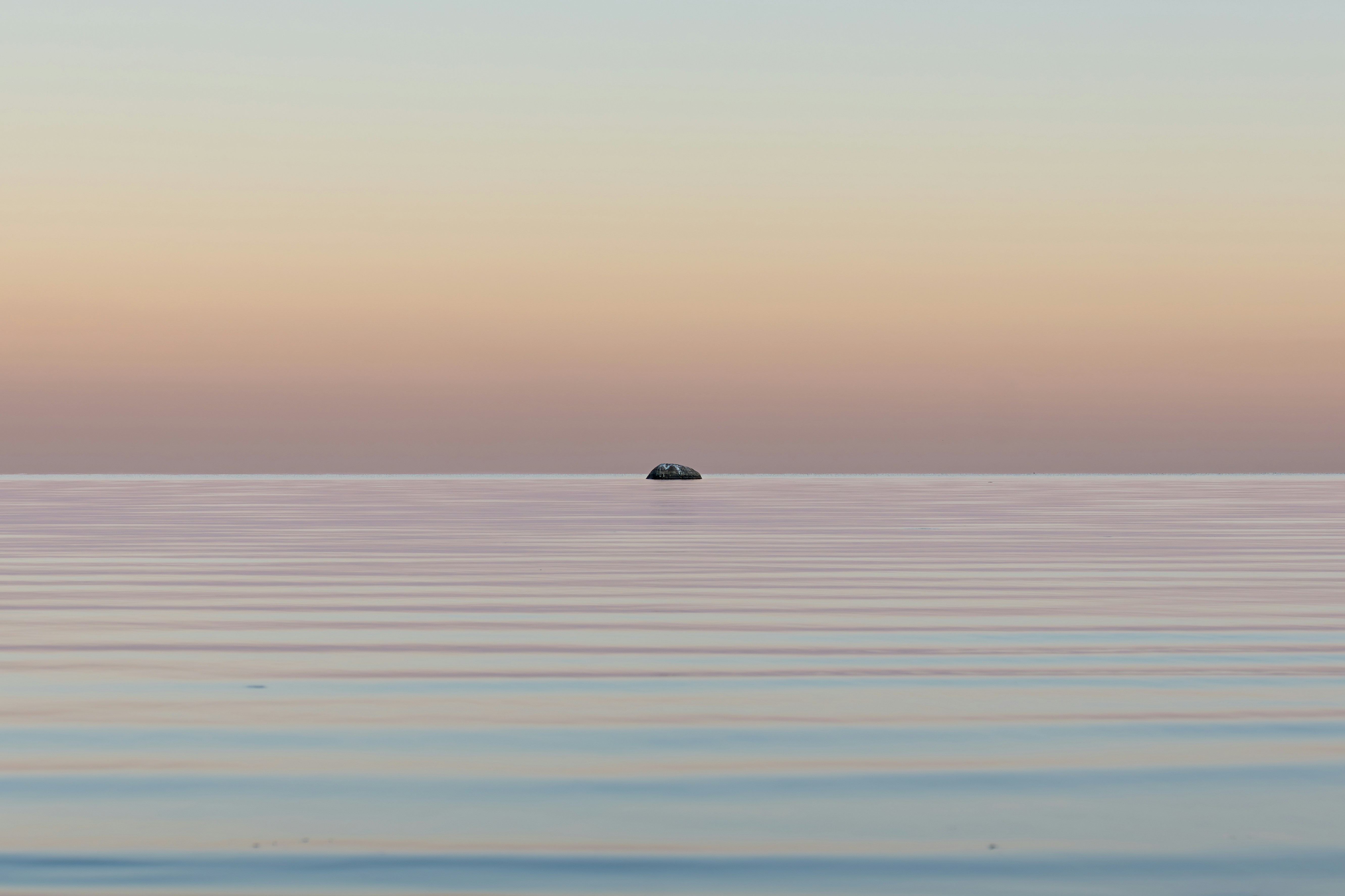 Serenity on the Horizon: A Solitary Rock Amidst Tranquil Waters