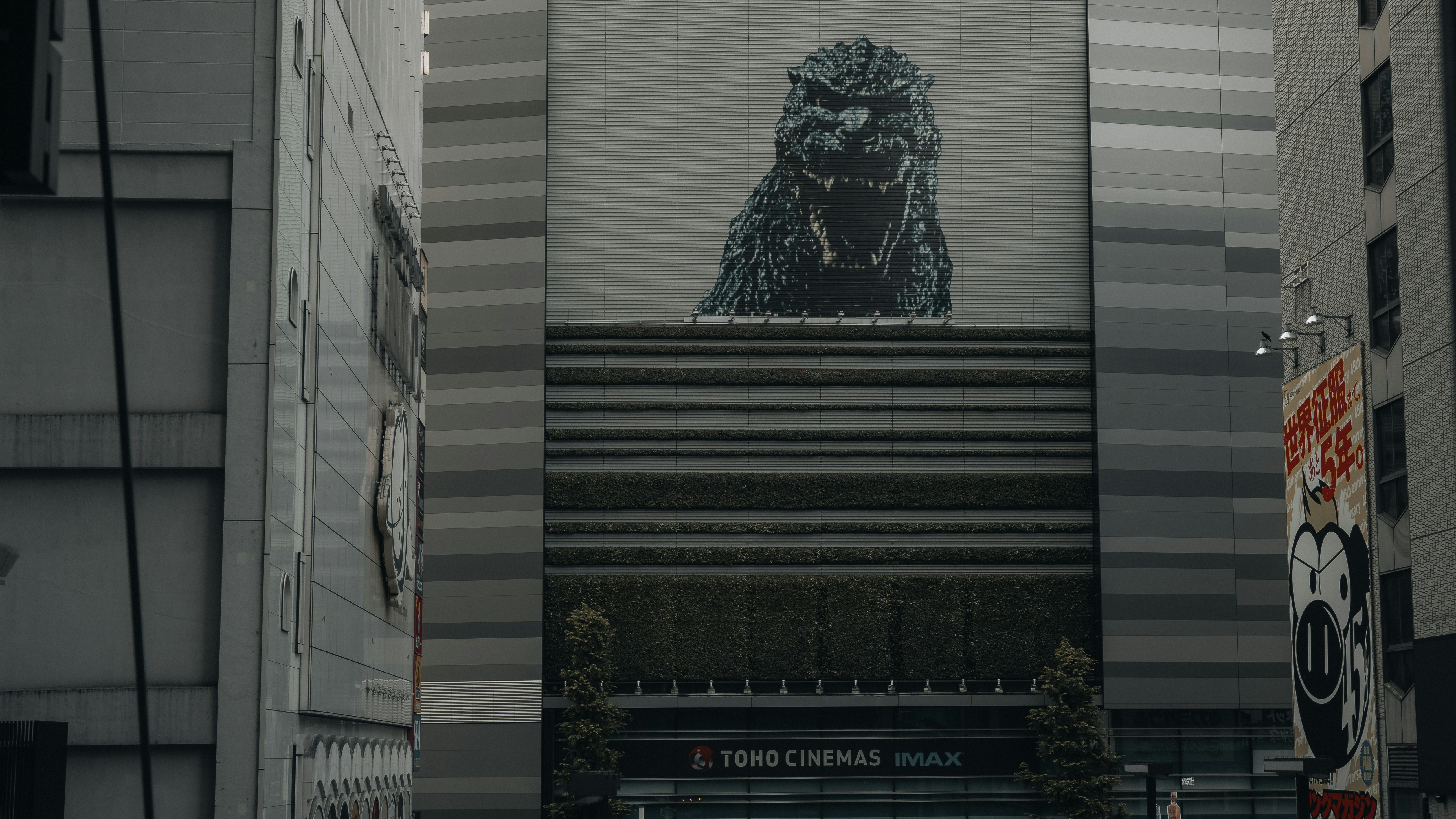 A striking mural of Godzilla dominates the facade of a cinema, showcasing the iconic monster in a dramatic pose. The urban setting enhances the mural's impact.