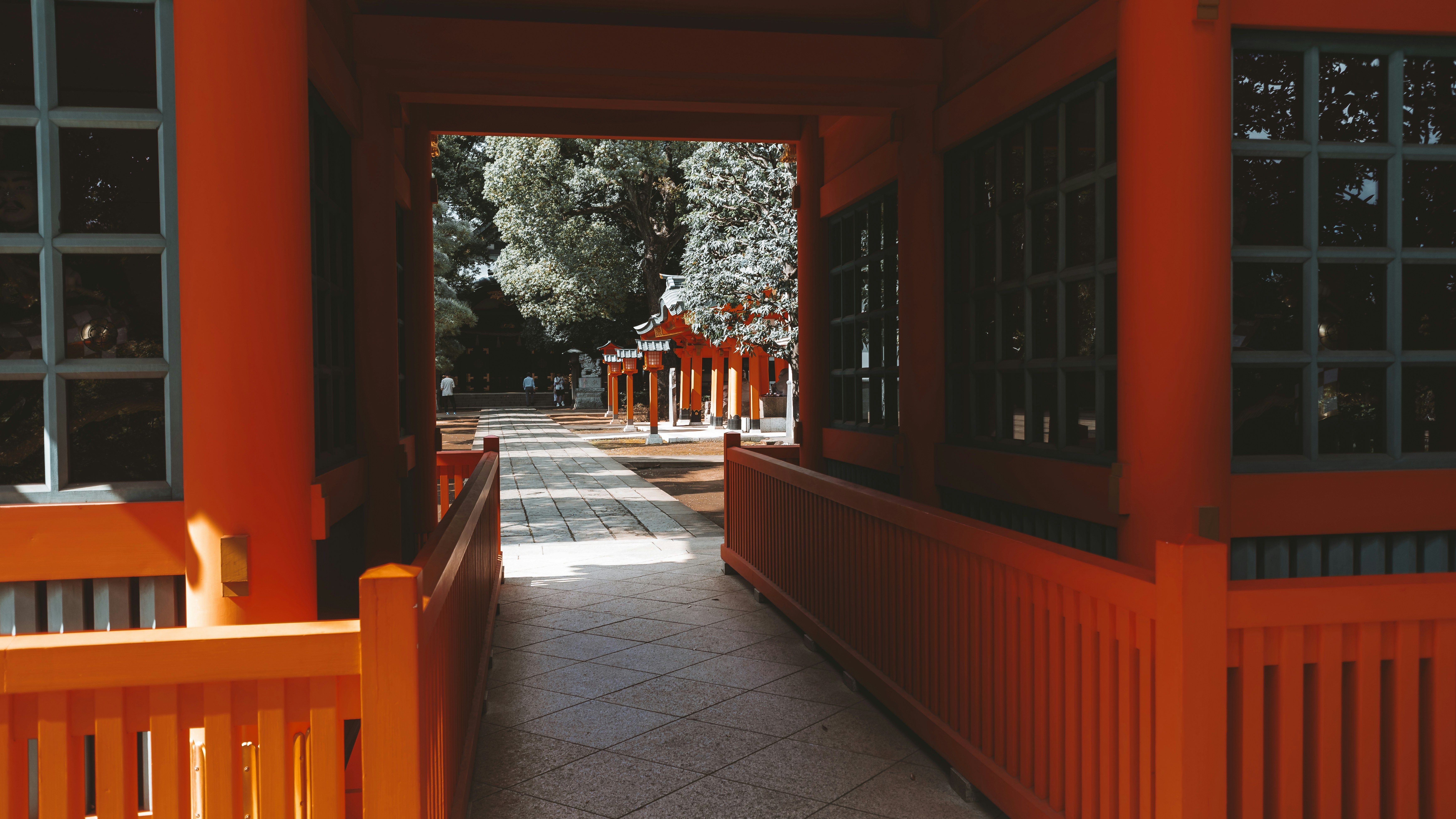 A serene walkway framed by striking orange architecture, leading to traditional structures in a tranquil setting.