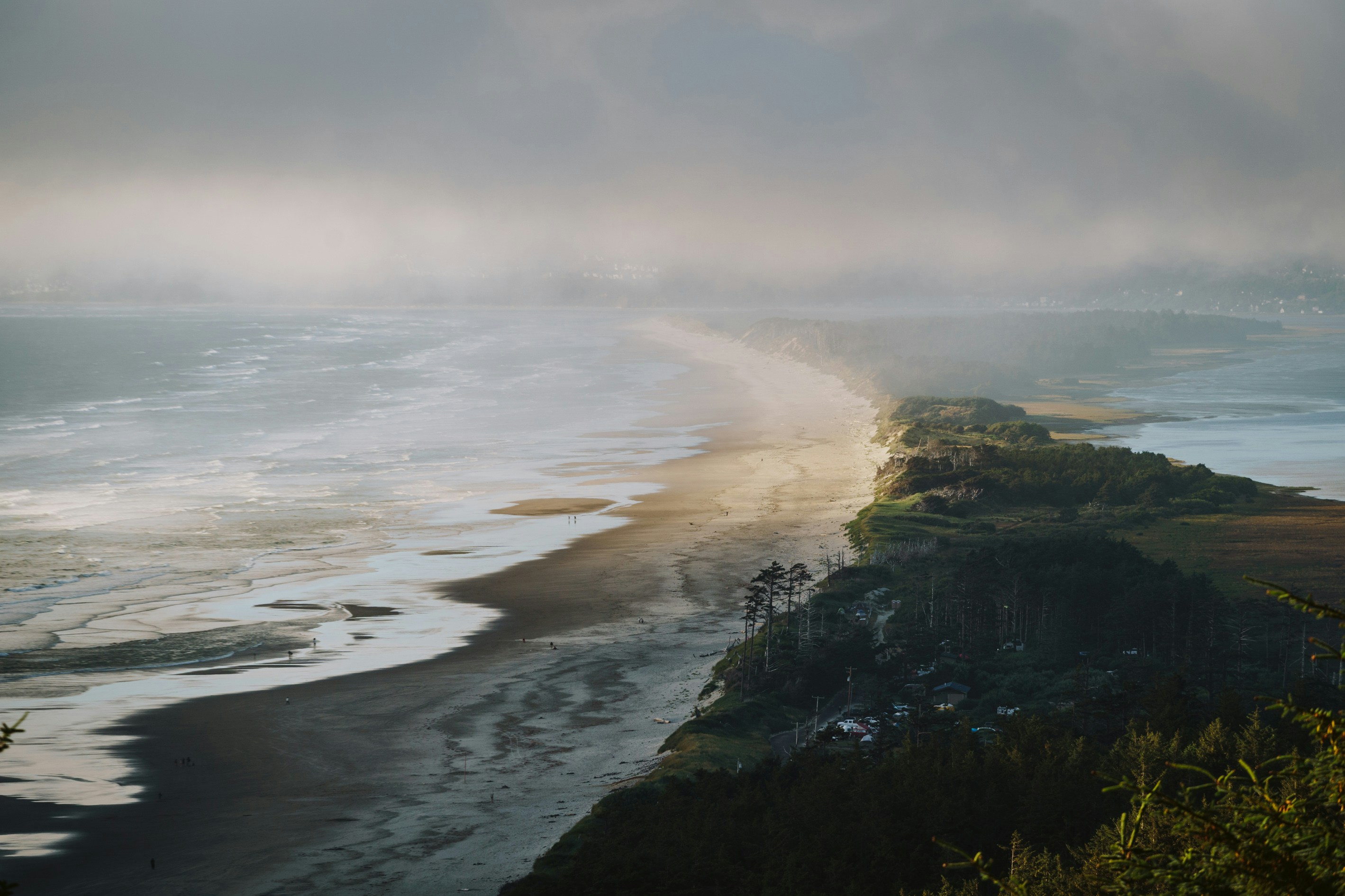 Misty coastal landscape with a winding shoreline and gentle waves lapping at the sandy beach under soft light.