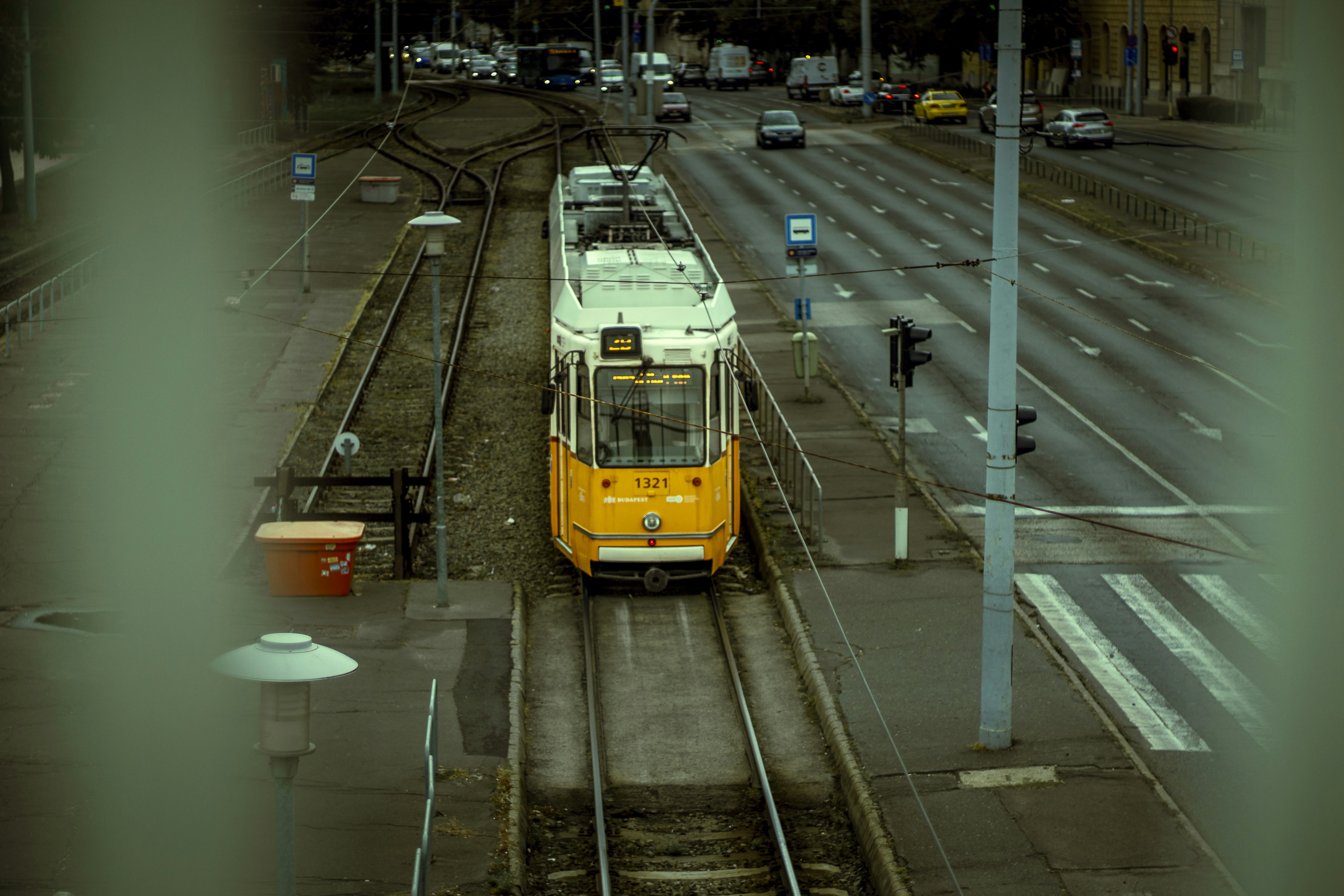 Tram approaching a stop on a bustling city street, surrounded by traffic and urban infrastructure.