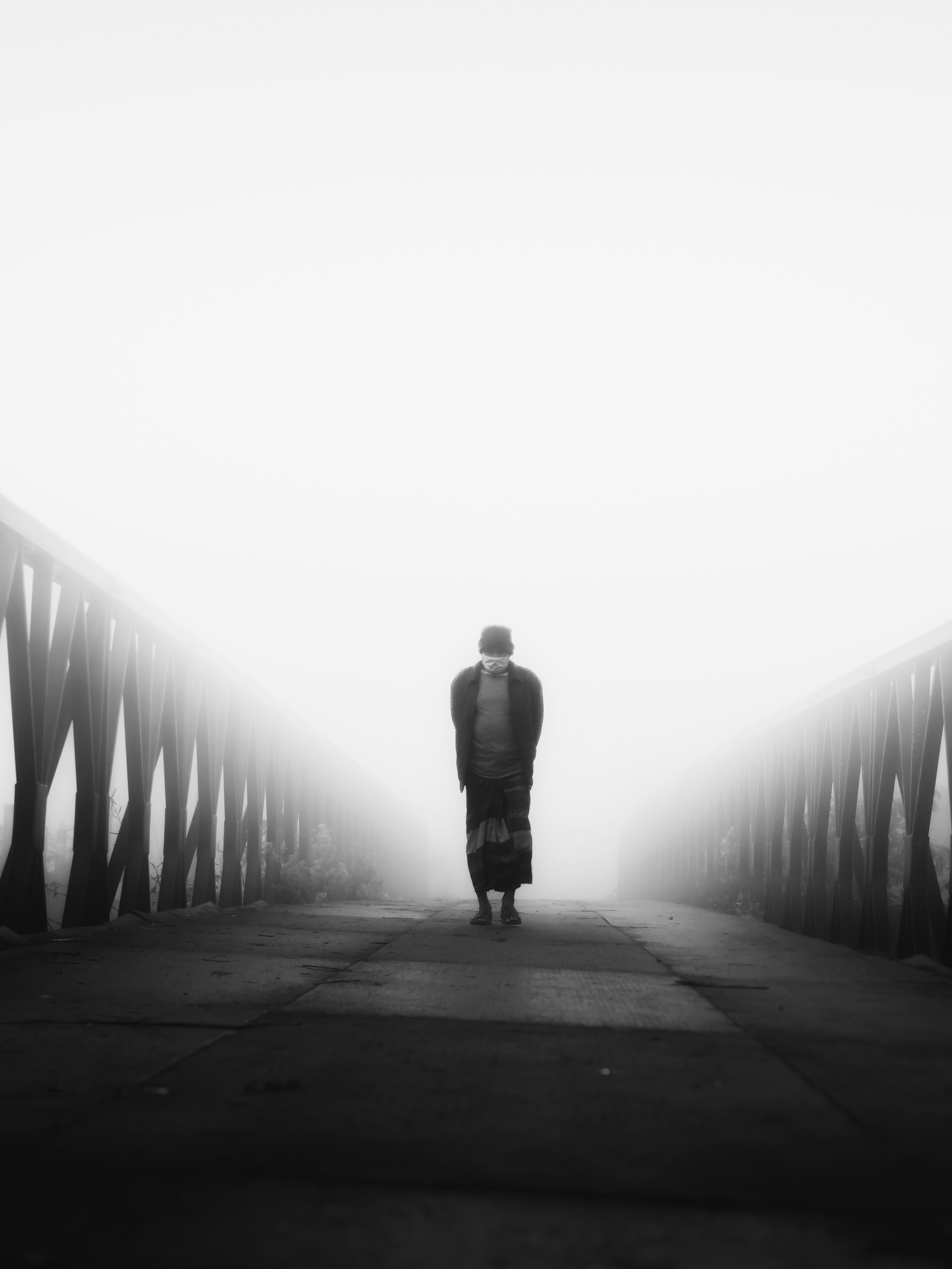 An old man walking across an iron bridge on a foggy winter morning in Bangladesh, wearing a sweater and a woolen cap