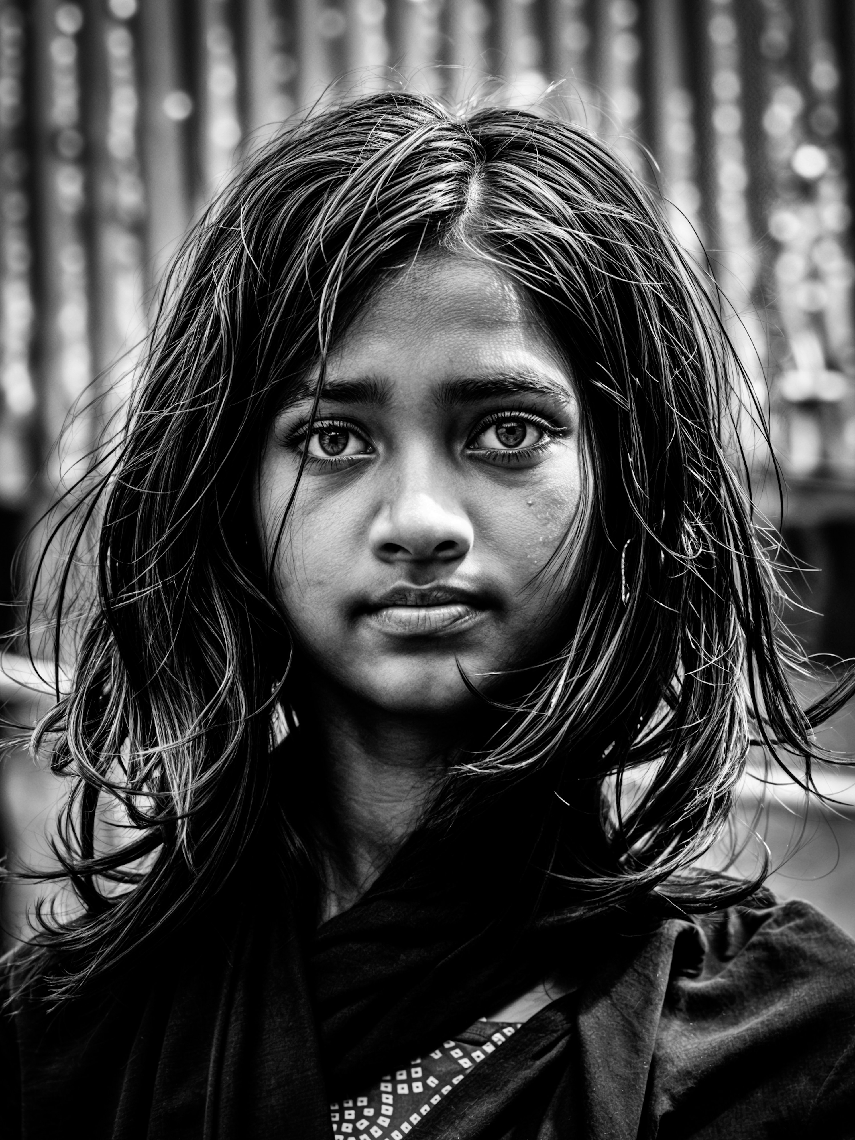 A young girl with tousled hair gazes intently, her expression revealing a depth of emotion. The monochrome tones enhance the intensity of her eyes.