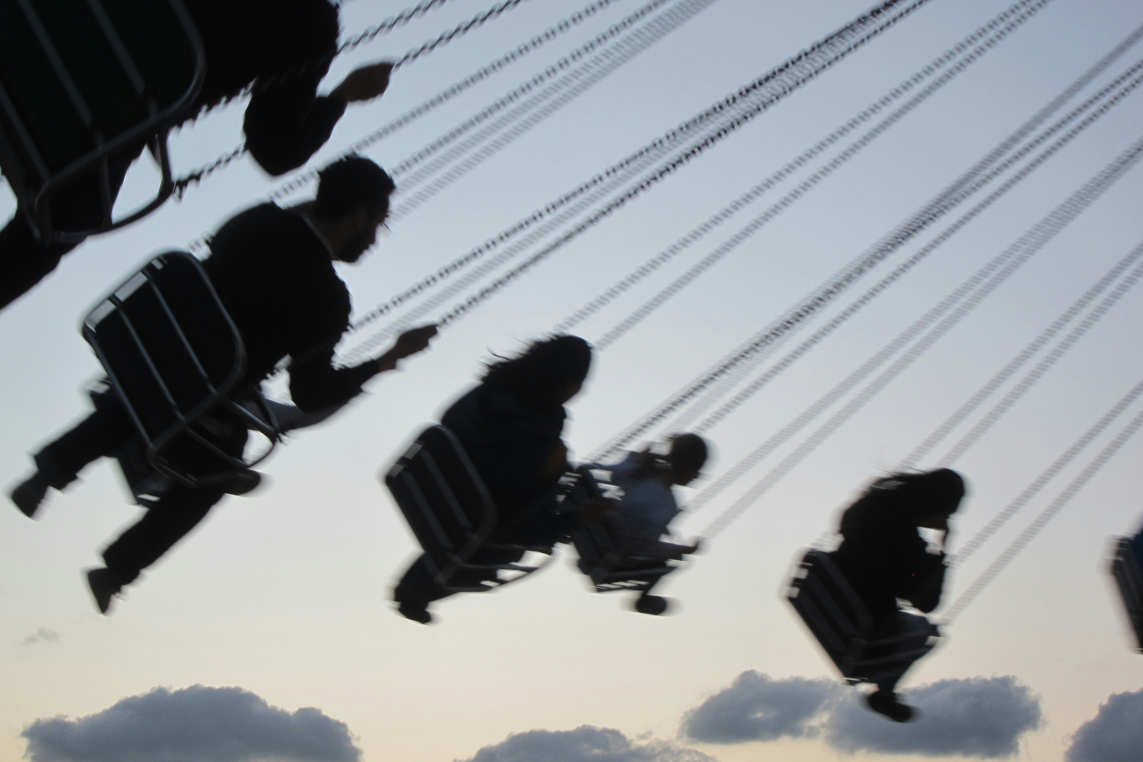 Silhouetted figures in a swing ride against a twilight sky, capturing the thrill of amusement park fun.