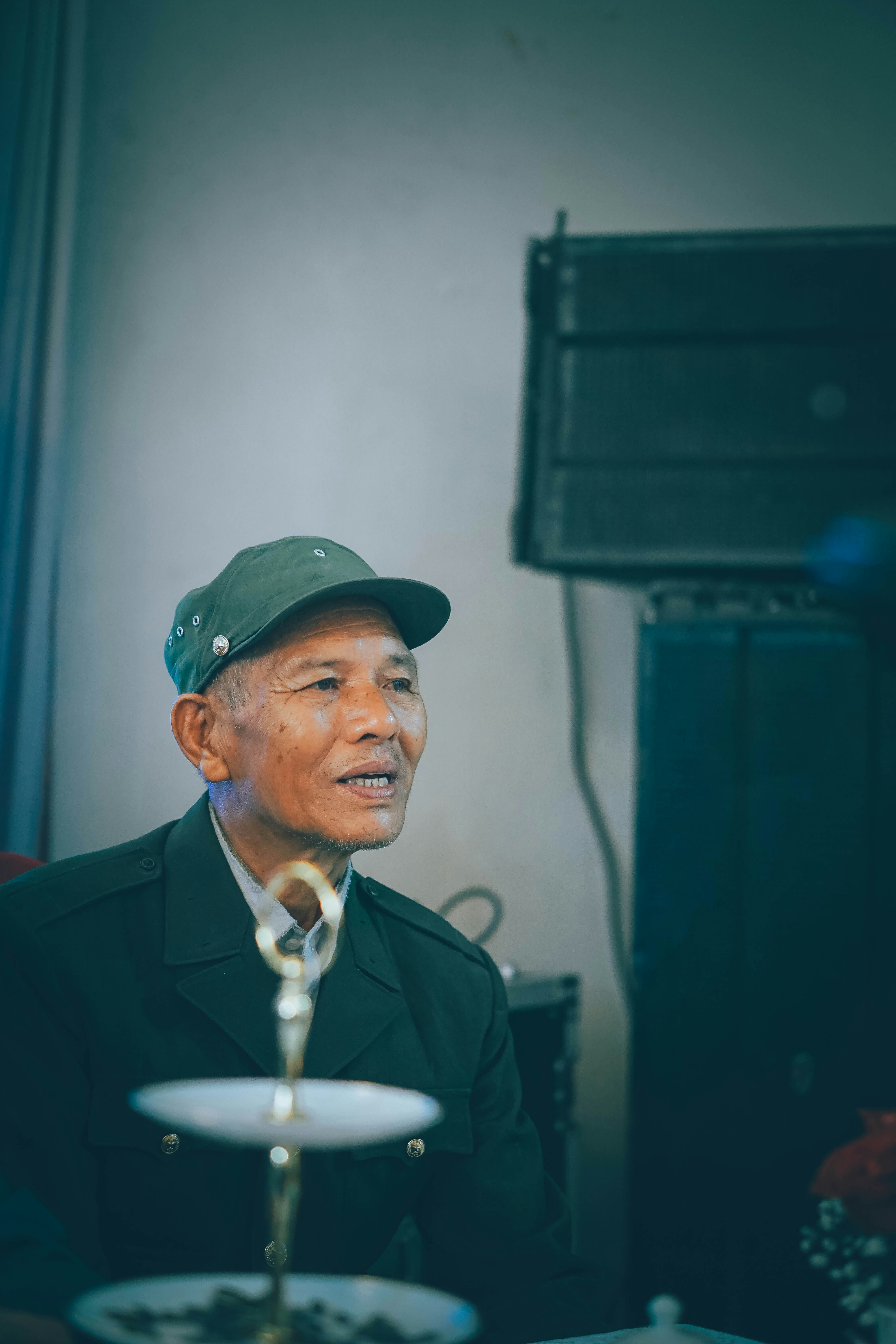 Green-Cap Portrait in Soft Indoor Light, Framed by a Subtle Tiered Stand