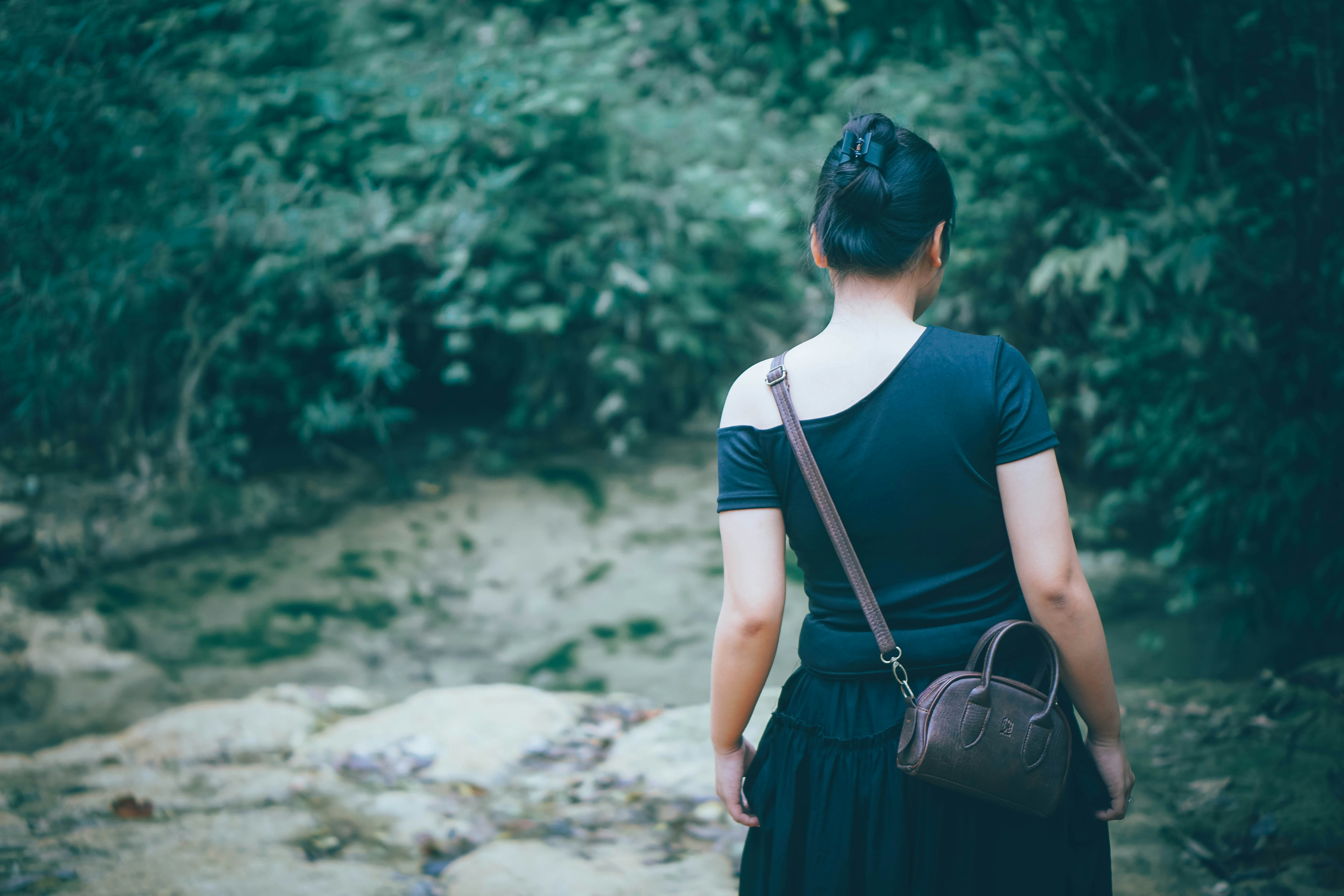 A woman stands with her back to the camera, gazing into a lush, green landscape, embodying a moment of reflection. The scene captures the tranquility of nature.