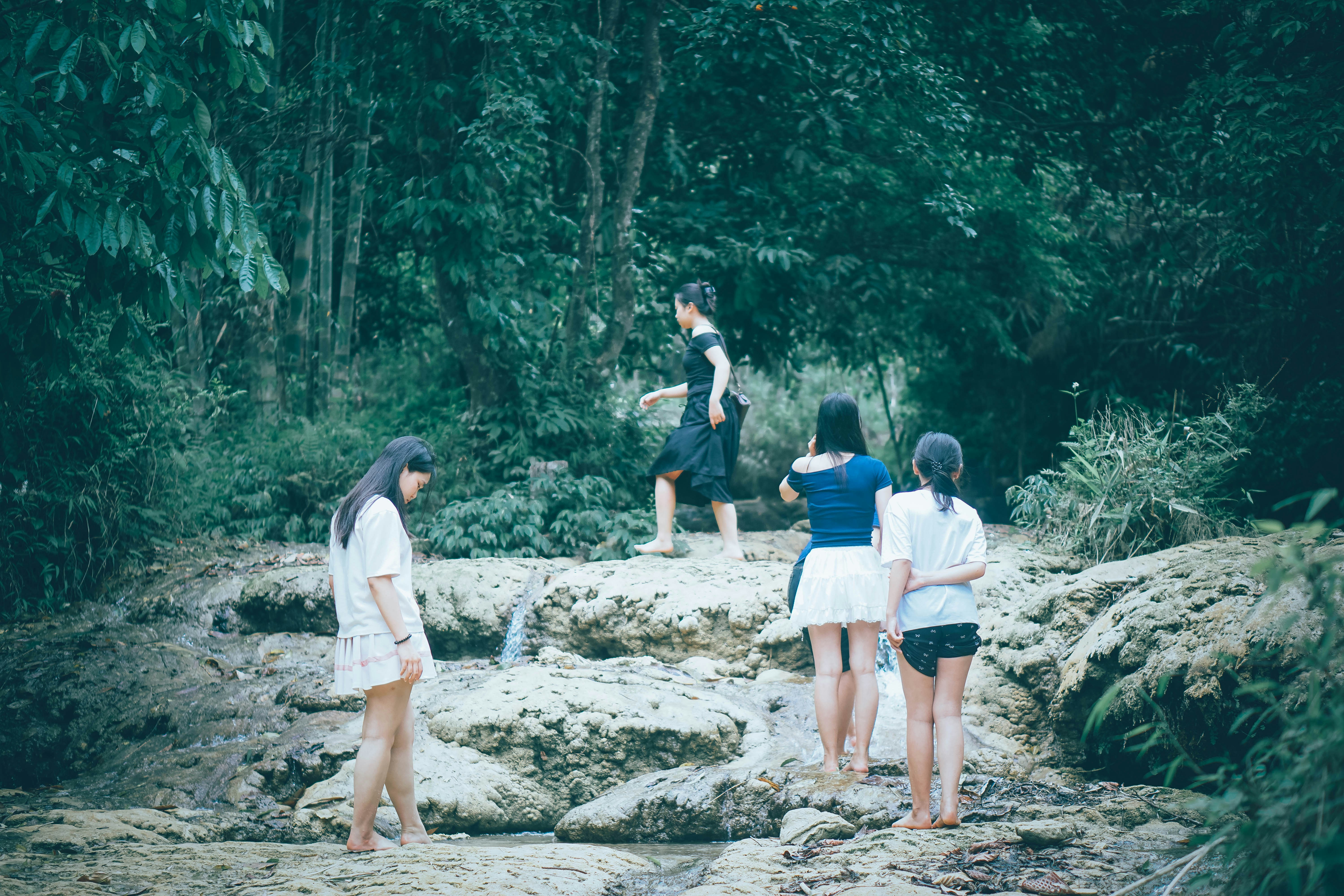 Four girls exploring a rocky stream in a lush forest, immersed in nature's tranquility.