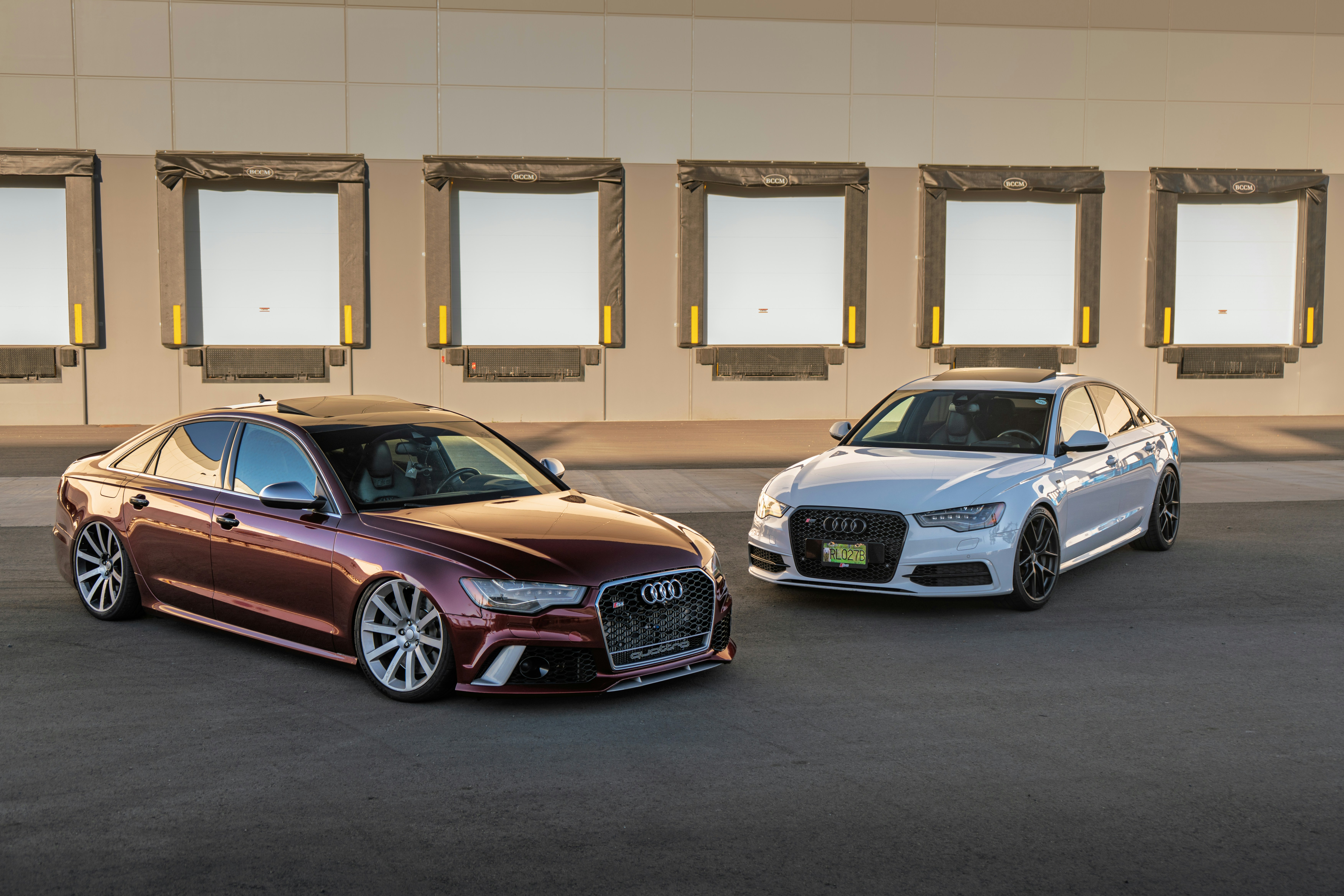 Two modified Audi sedans parked in a well-lit industrial space, highlighting their sleek designs and custom features.
