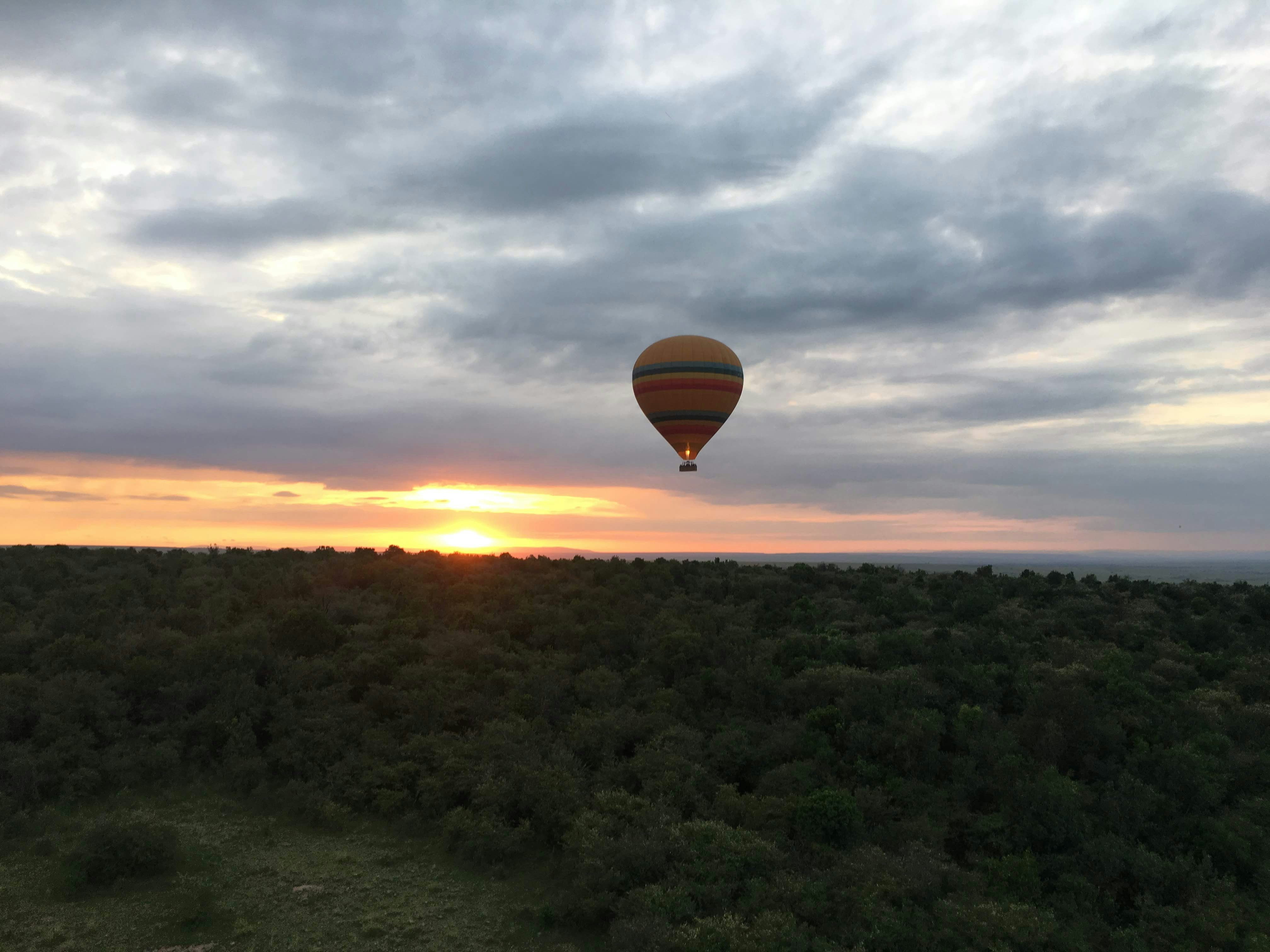 Hot air balloon flying over landscape at sunset