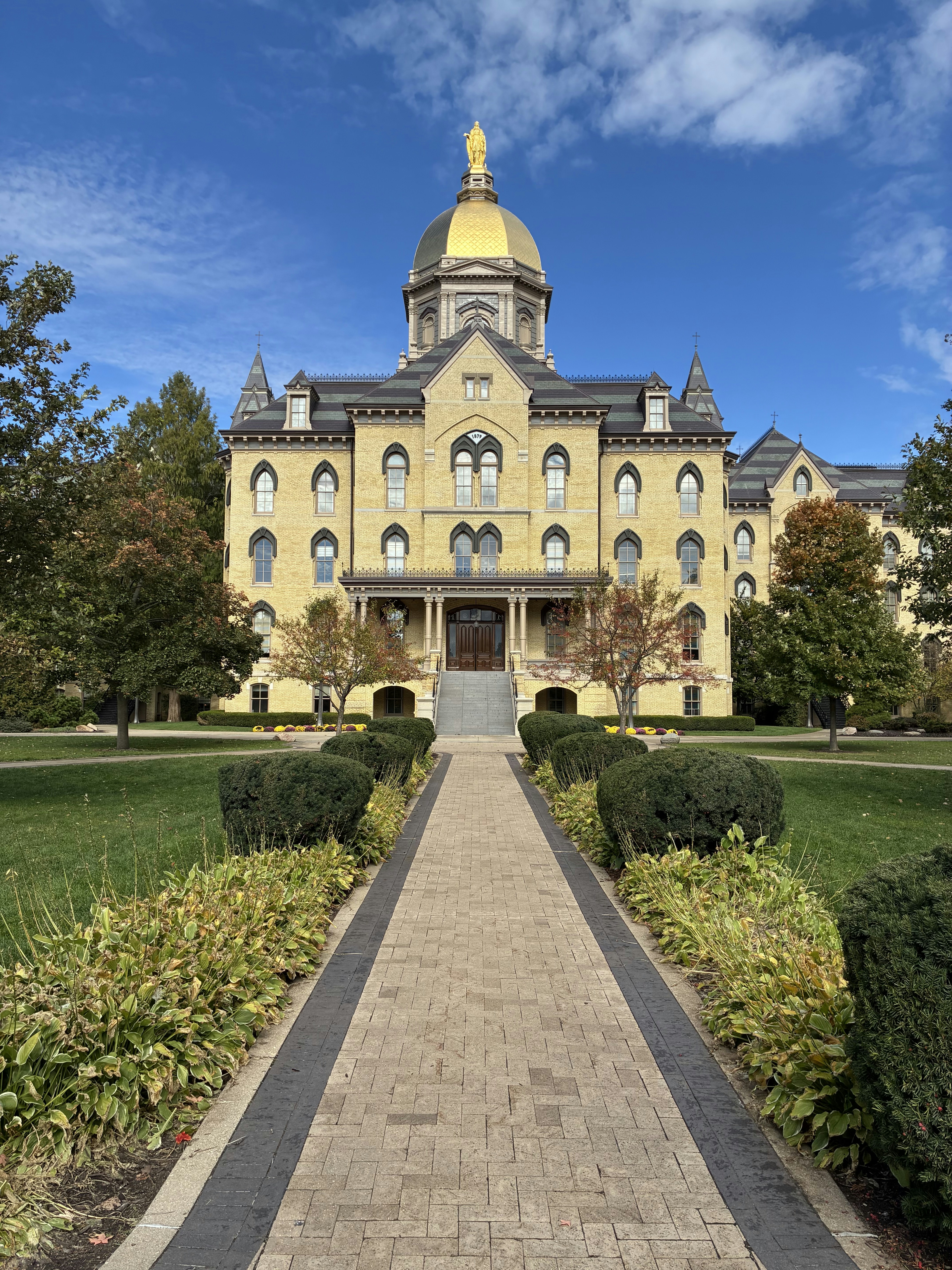 Historic university building with a golden dome, flanked by lush greenery and a well-defined pathway leading to the entrance.