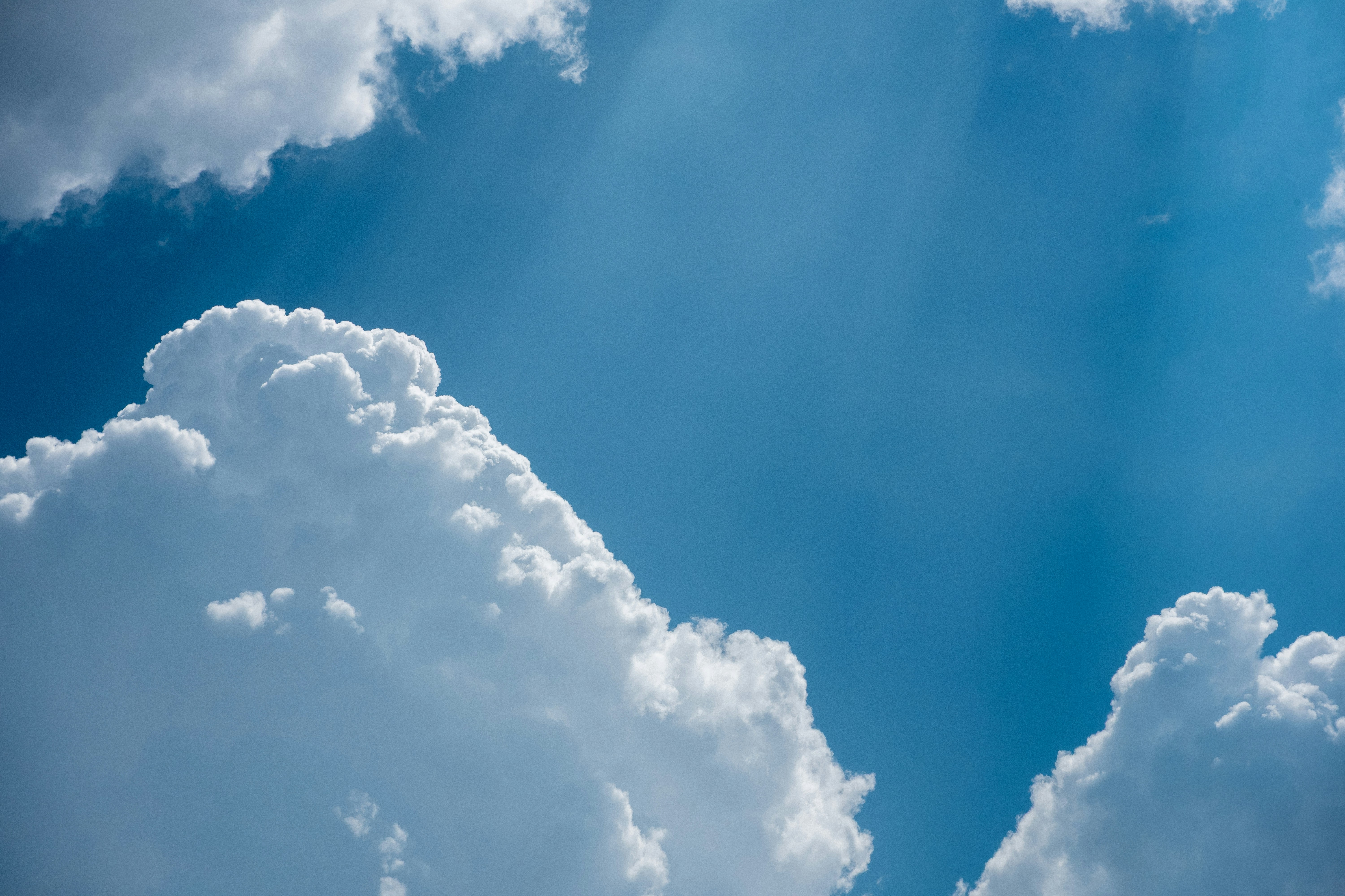 A blue sky filled with towering white clouds, softly lit by the sun. | Sunlight streaming through fluffy white clouds in blue sky