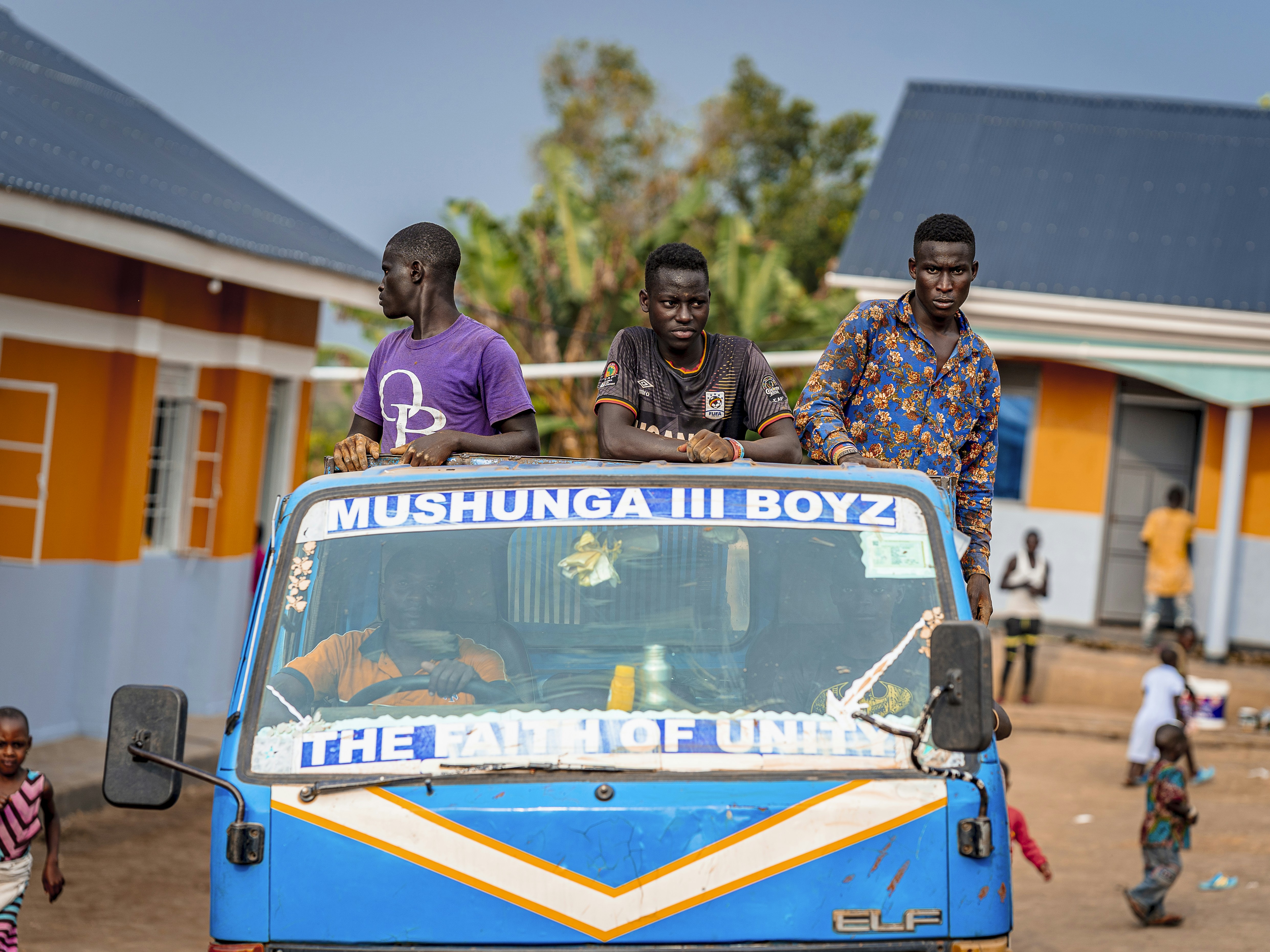 Three young men ride on top of a blue truck.