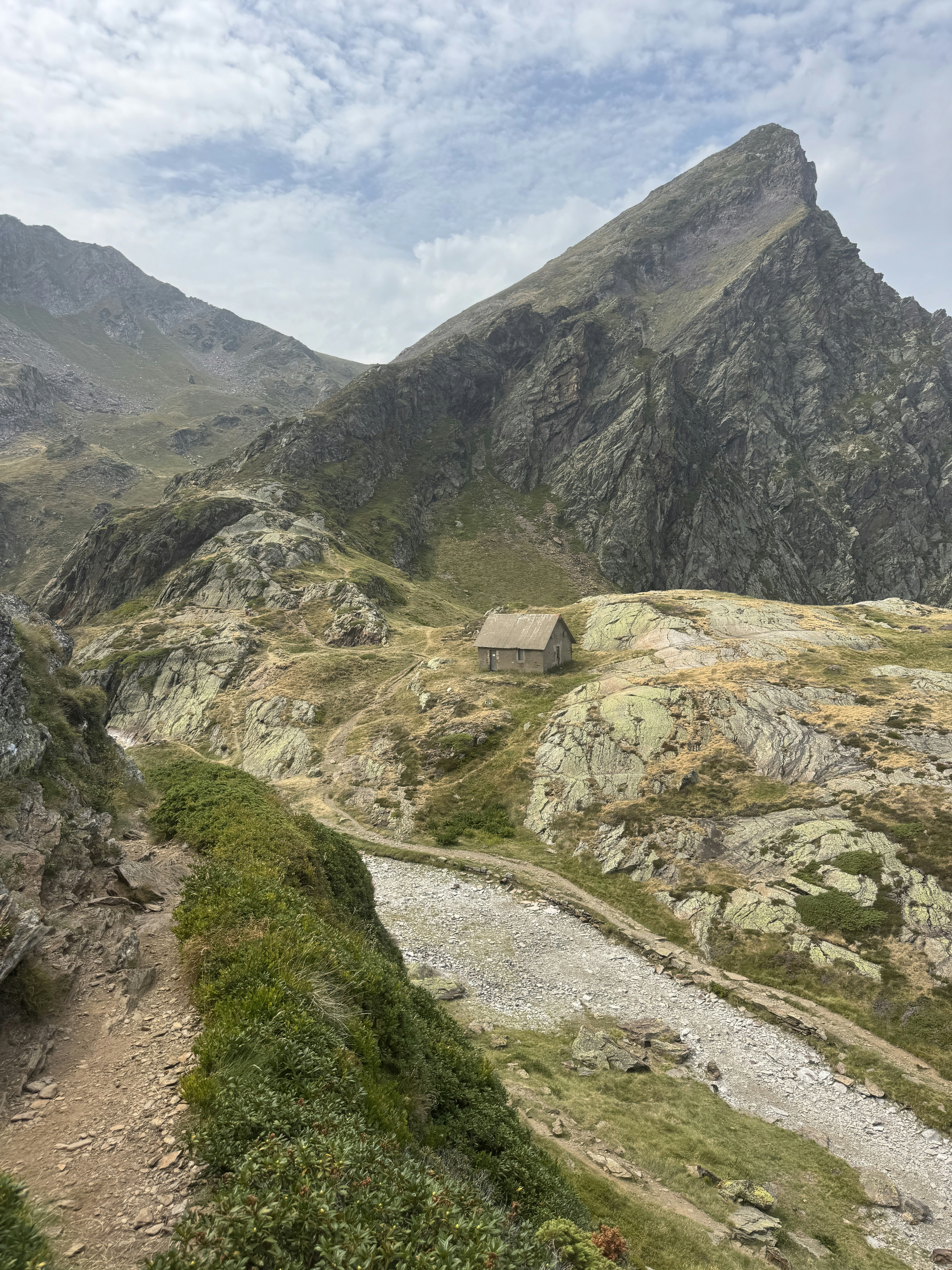 A rustic cabin nestled in a rocky landscape, surrounded by towering mountains and a winding path. The scene captures the essence of solitude in nature.