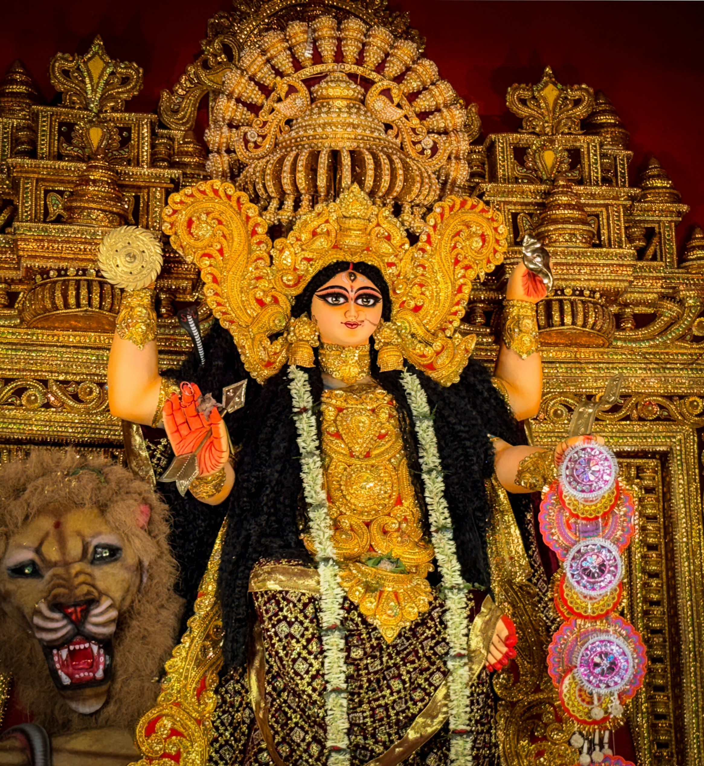Intricately adorned goddess statue with vibrant colors, surrounded by ornate decorations and a lion figure in the background.