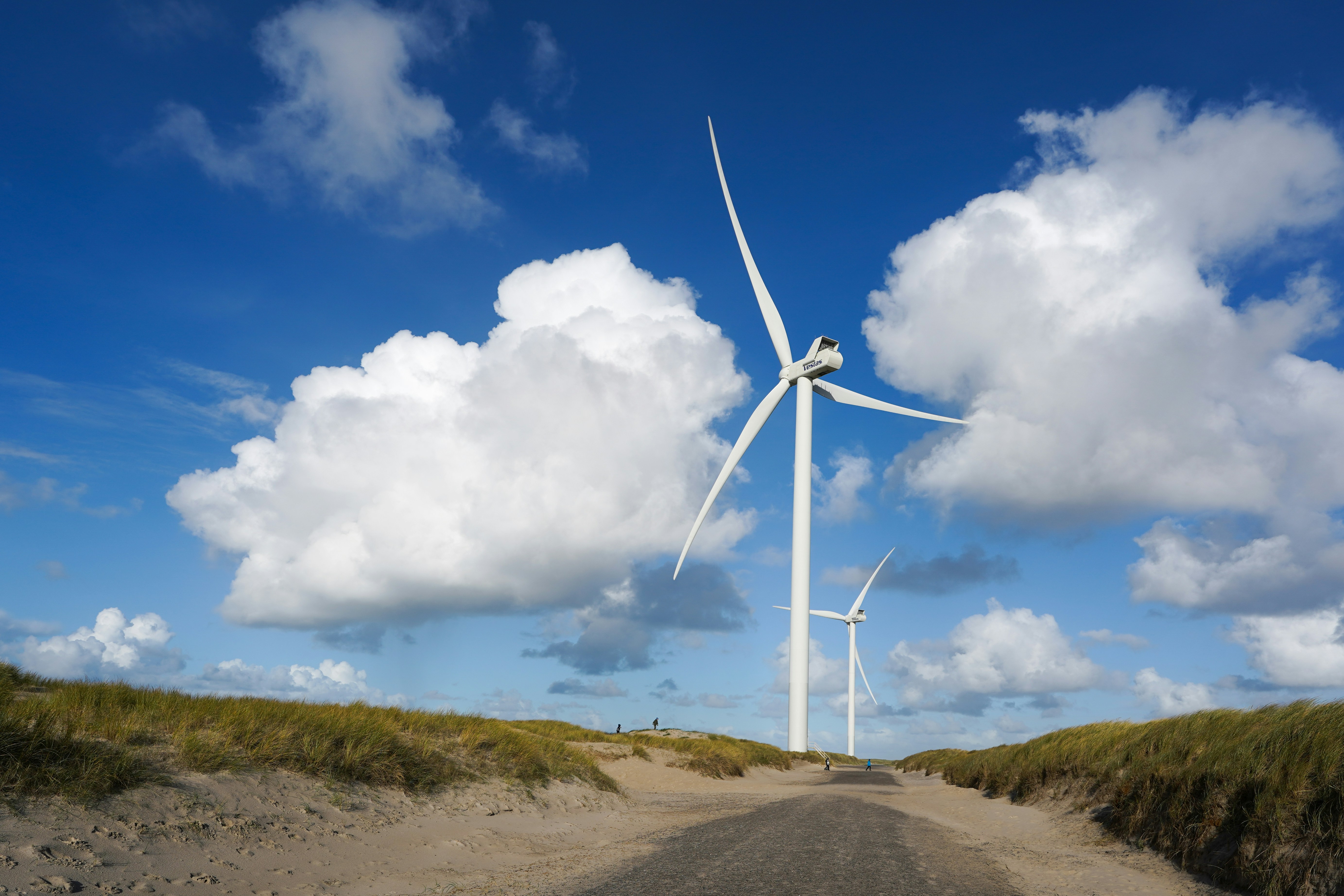 Wind turbines stand tall against a backdrop of fluffy clouds and a clear blue sky, illustrating the harmony between nature and renewable energy.