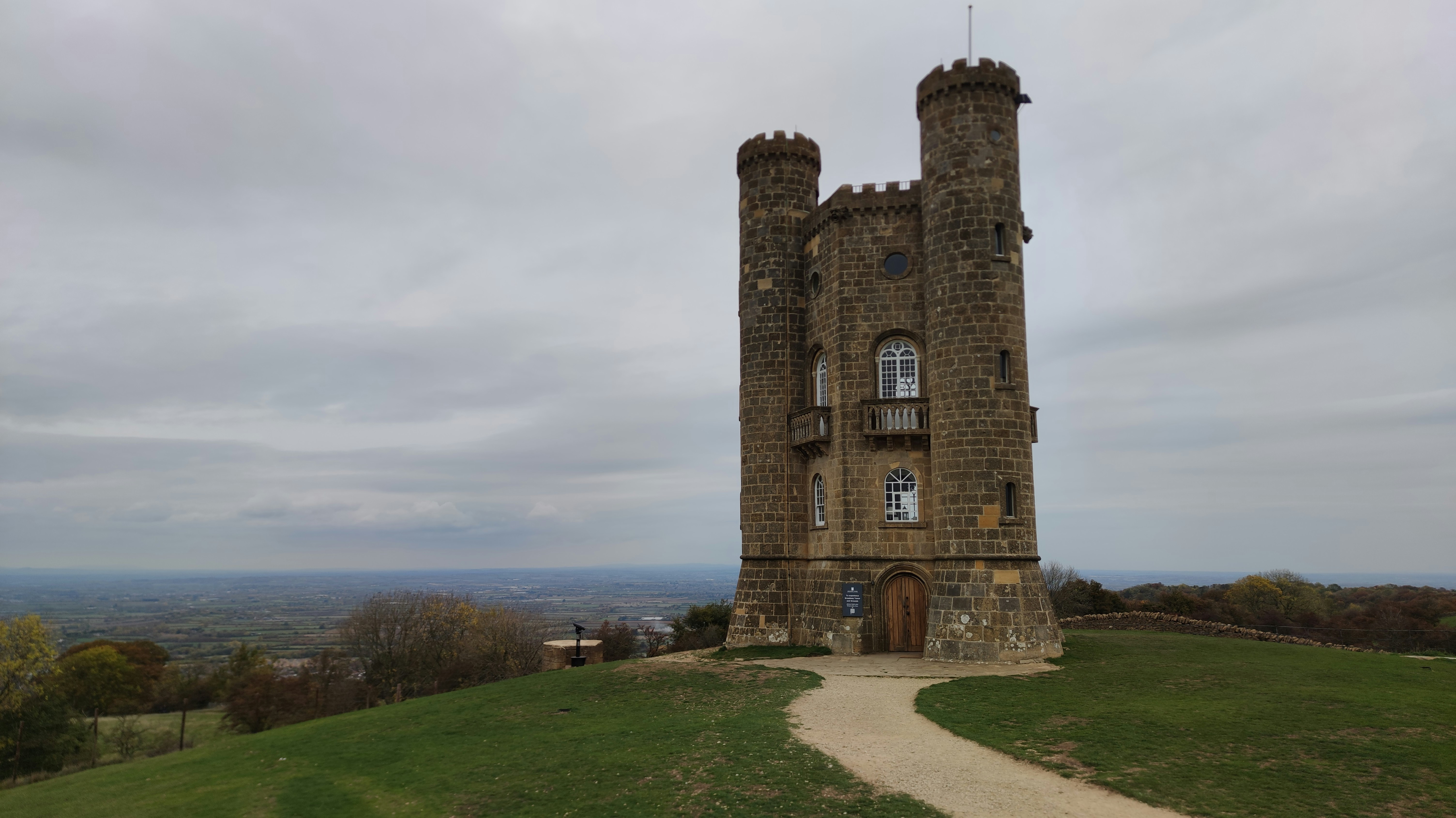 Historic stone tower stands majestically on a hillside, overlooking a vast valley under a cloudy sky.