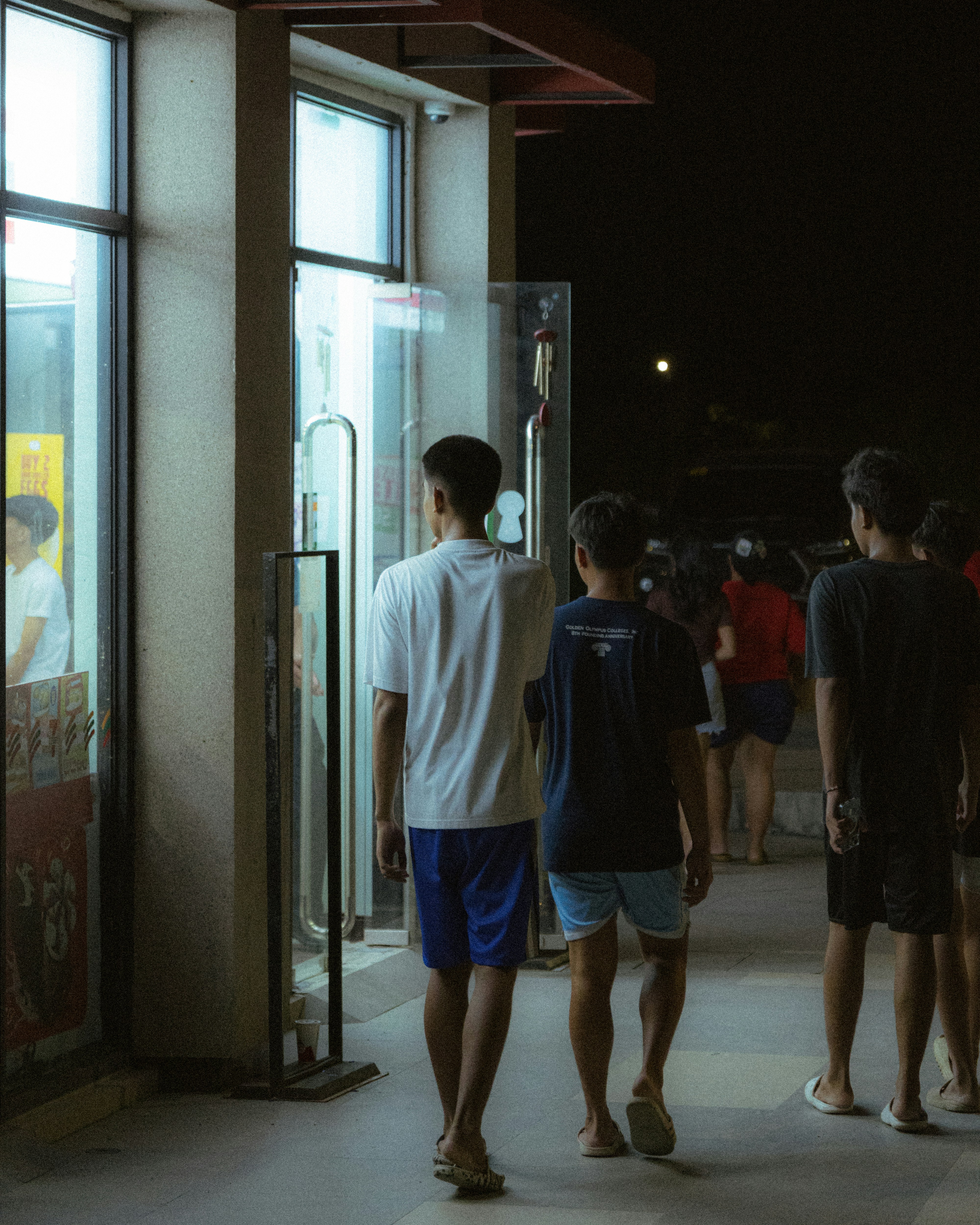 Young men walk at night near a building entrance.