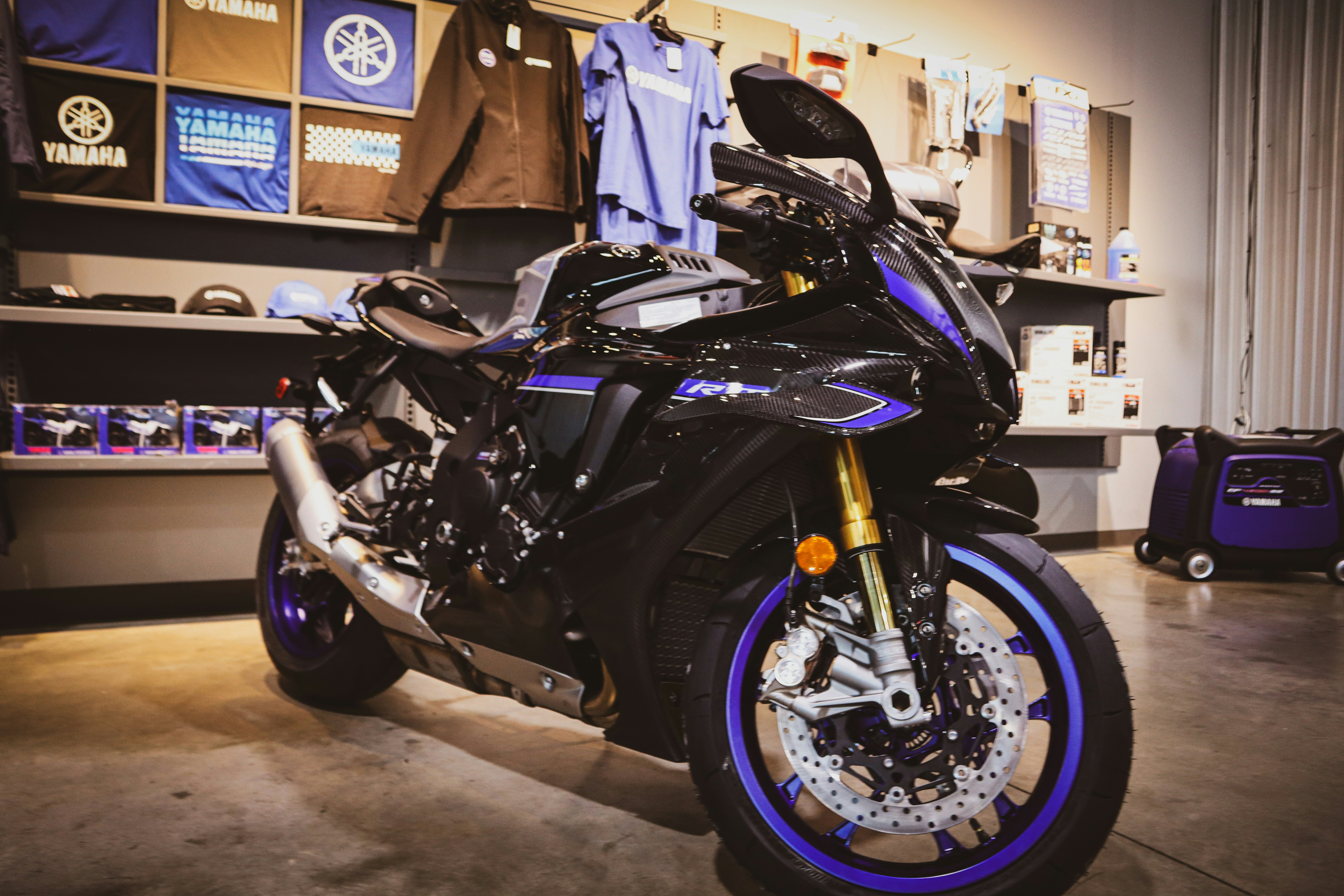 Sleek black Yamaha sportbike showcased in a modern showroom, surrounded by branded merchandise and apparel. The bike's dynamic design and striking colors draw attention.