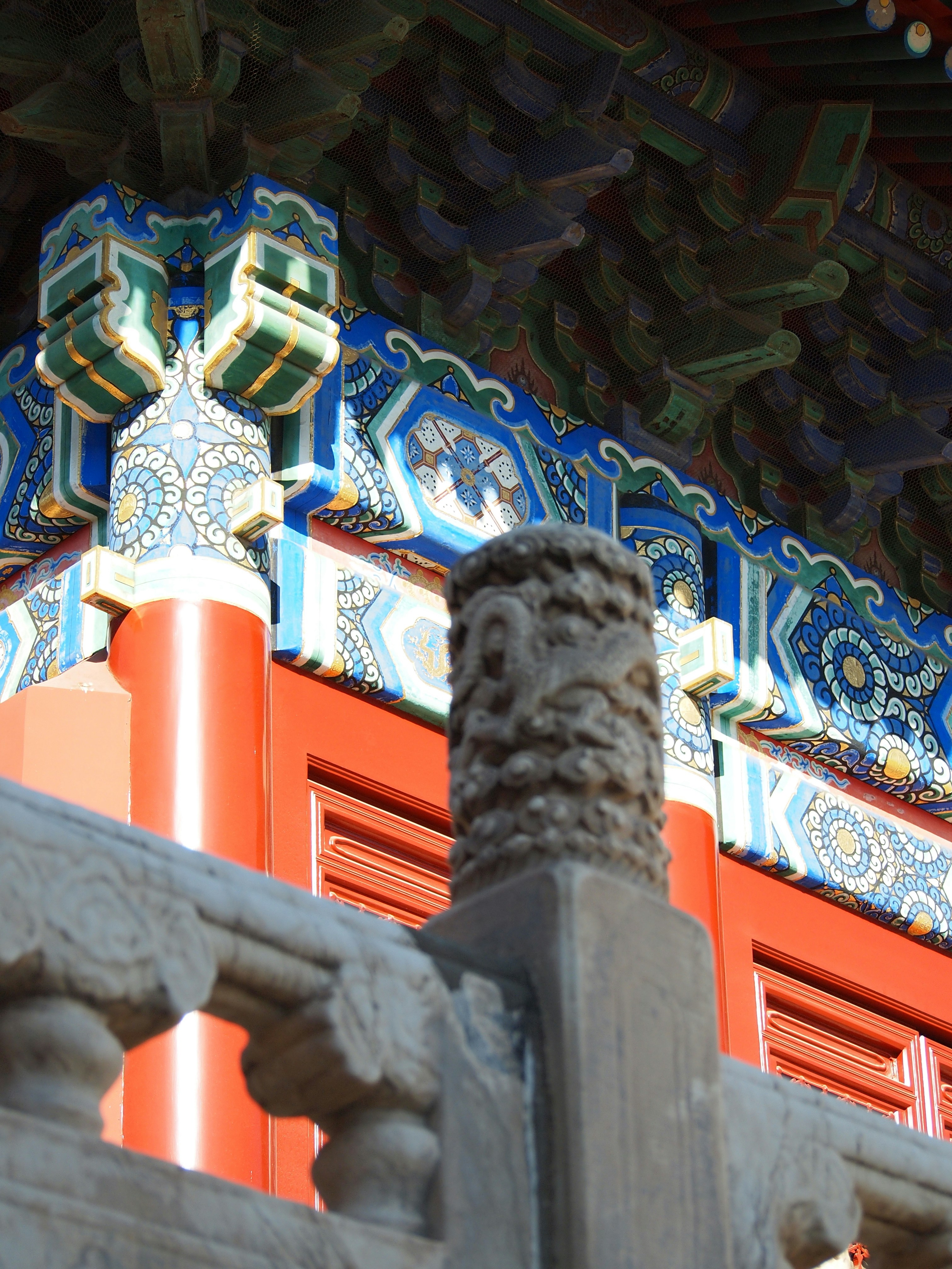 Intricate details of a traditional architectural facade featuring vibrant colors and ornate carvings. The stone pillar adds a historical context to the vibrant structure.