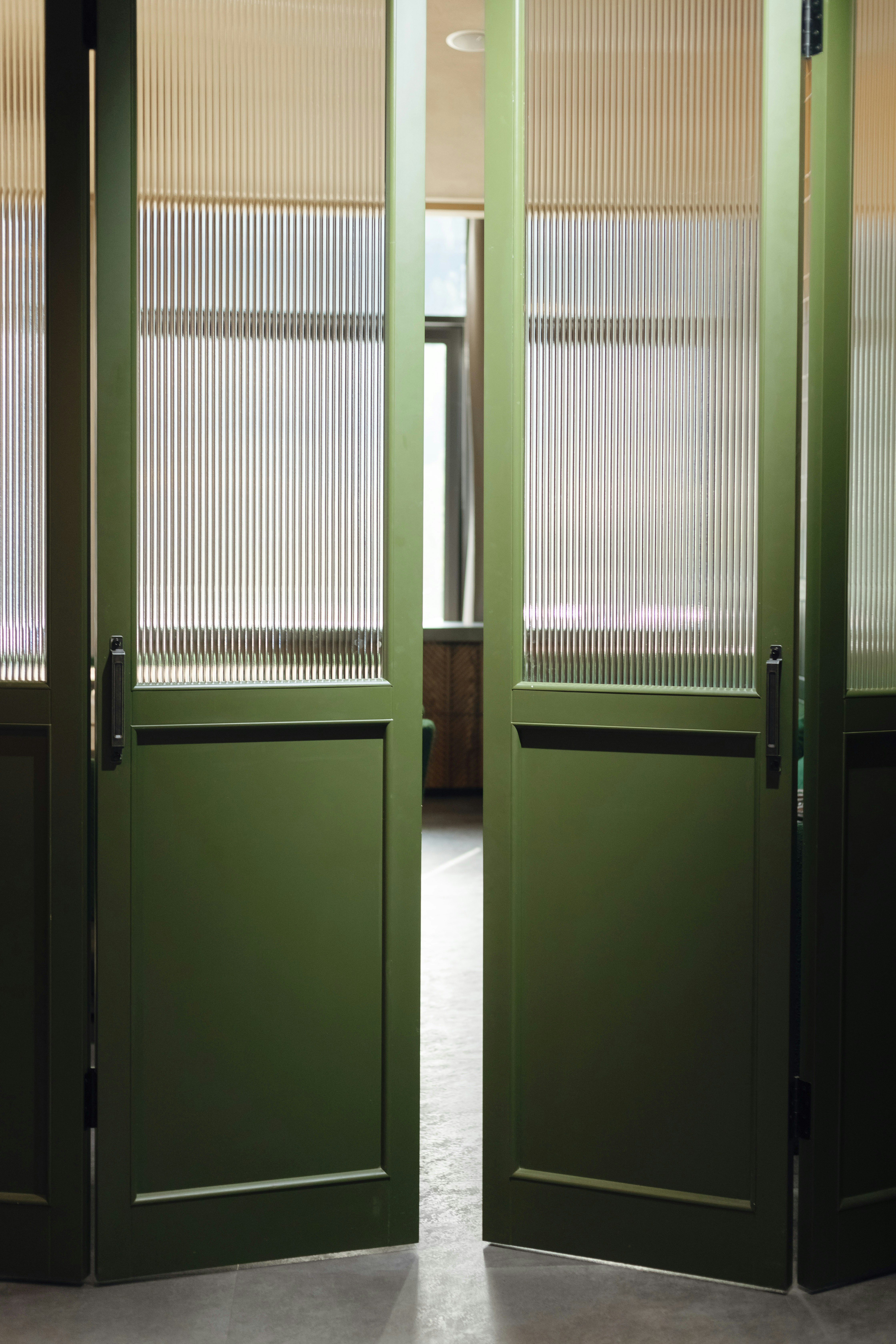 Two green doors with vertical glass panels open to reveal a softly lit interior space.