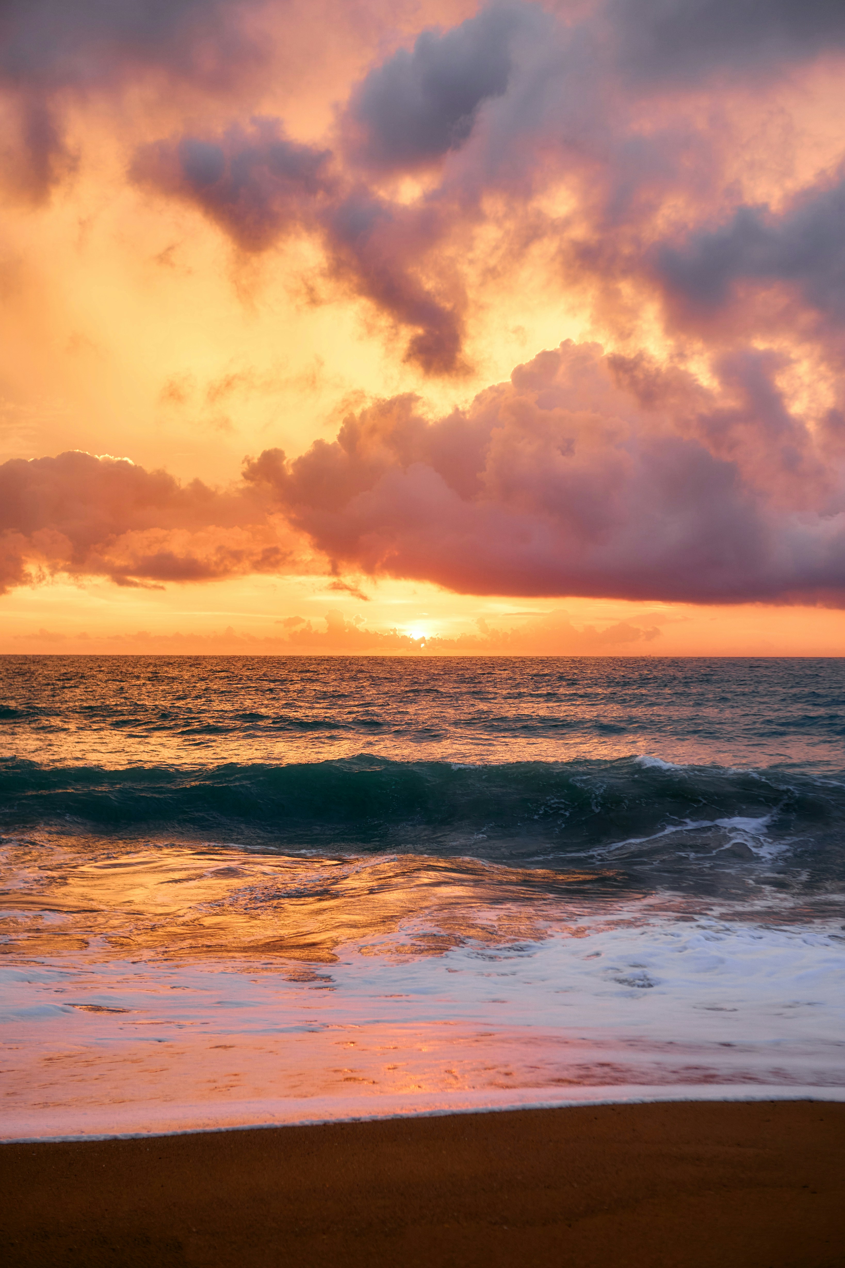 Vibrant sunset reflecting on ocean waves with dramatic clouds above, creating a serene coastal scene.